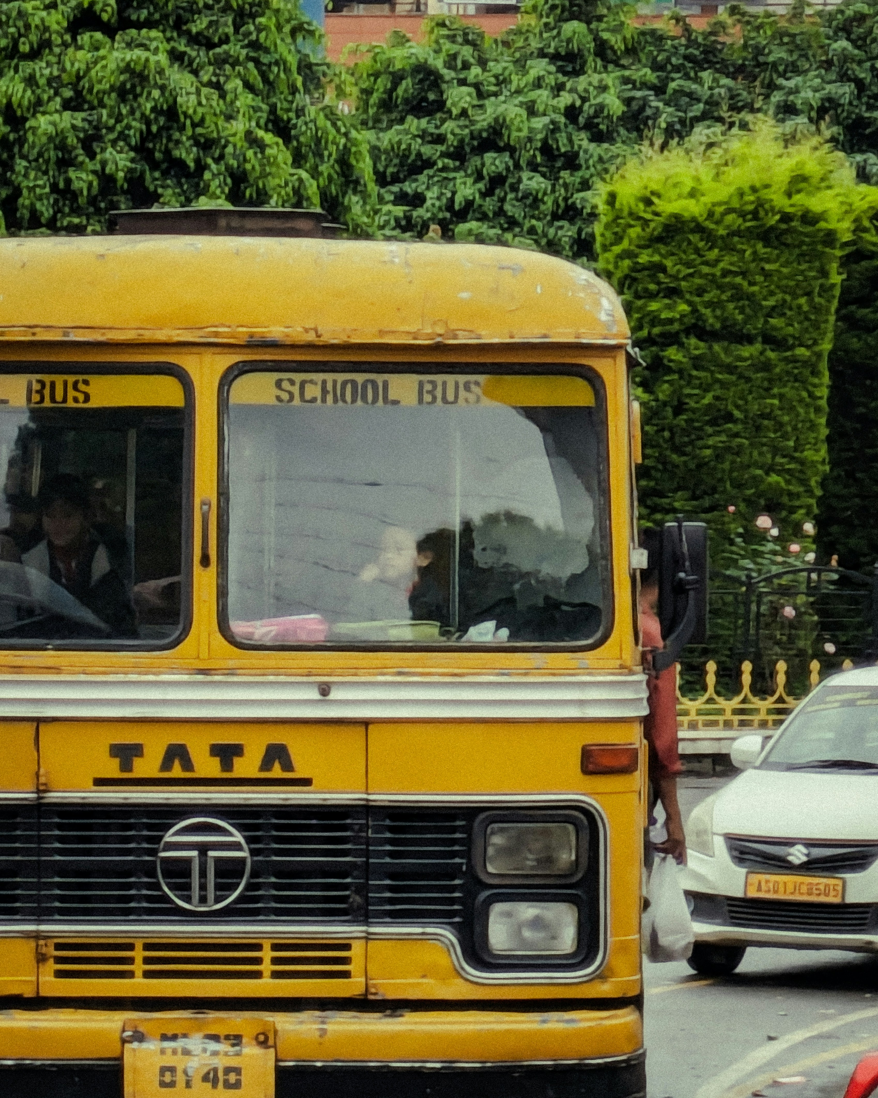 A yellow bus driving down a street next to a white car