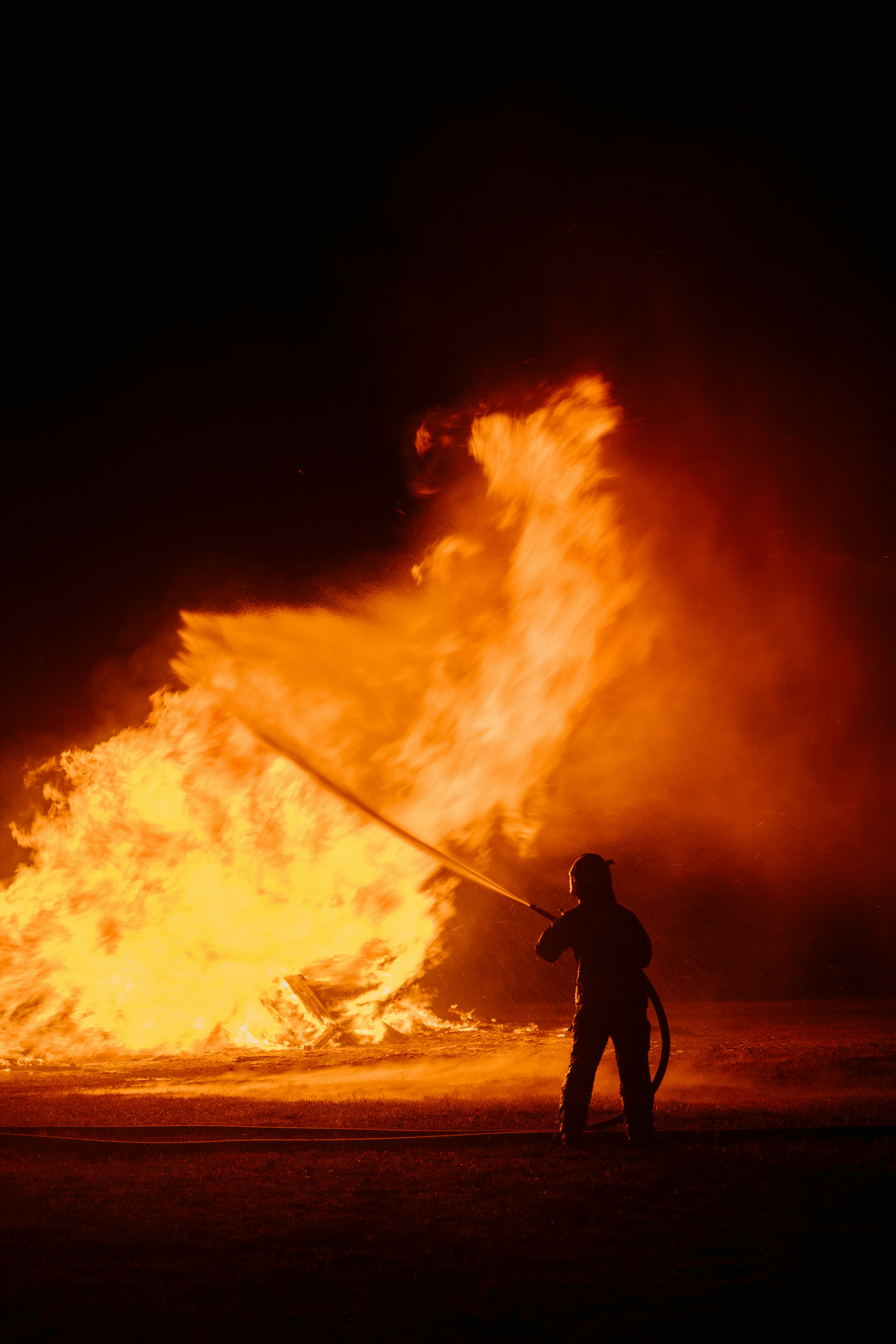 Firefighter battling a fierce blaze at night, illuminated by the flames. The dramatic scene captures the intensity of the moment.