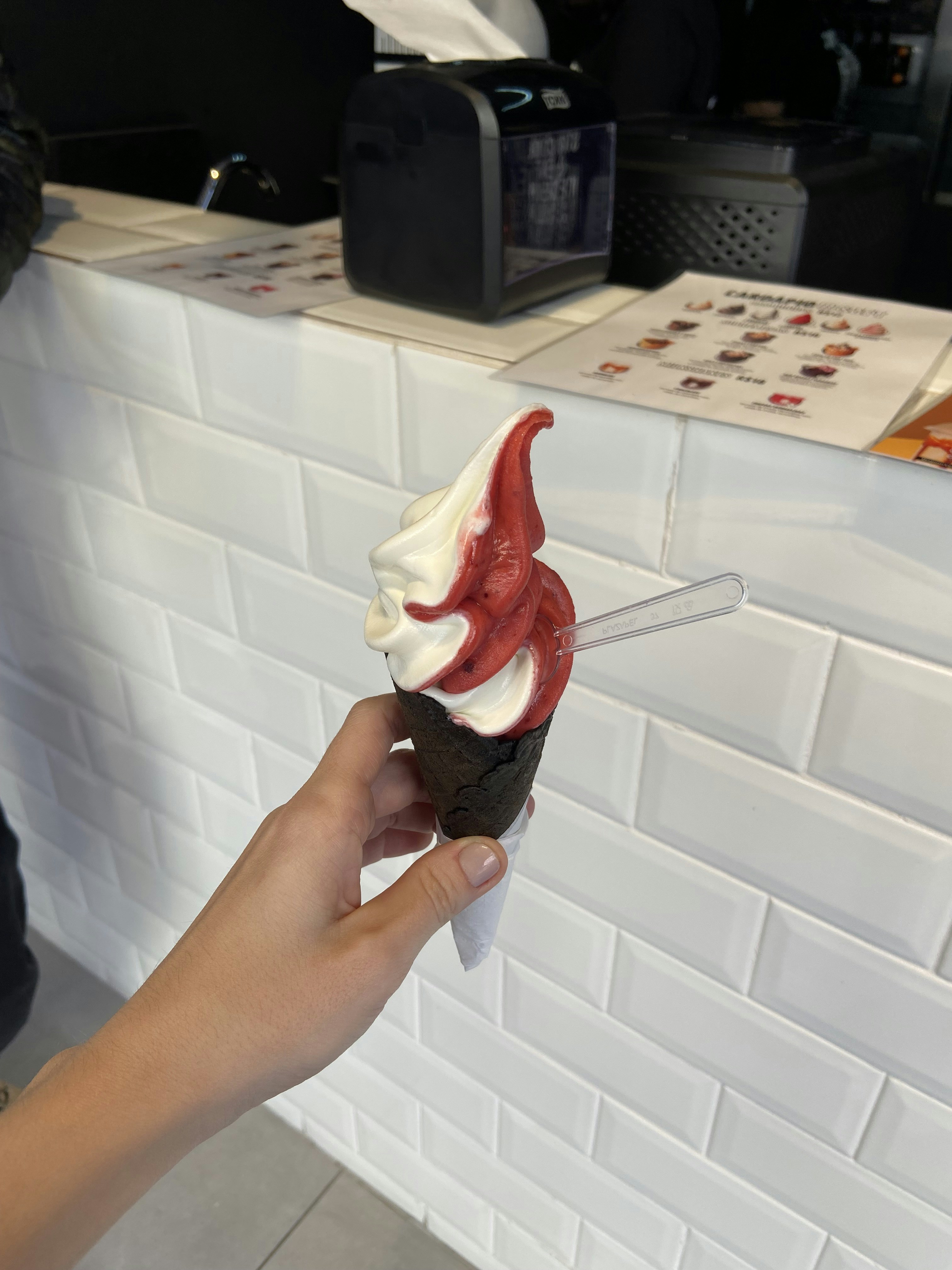 Crimson Swirl on a Midnight Cone: Hand-Held Soft Serve Against White Tiles