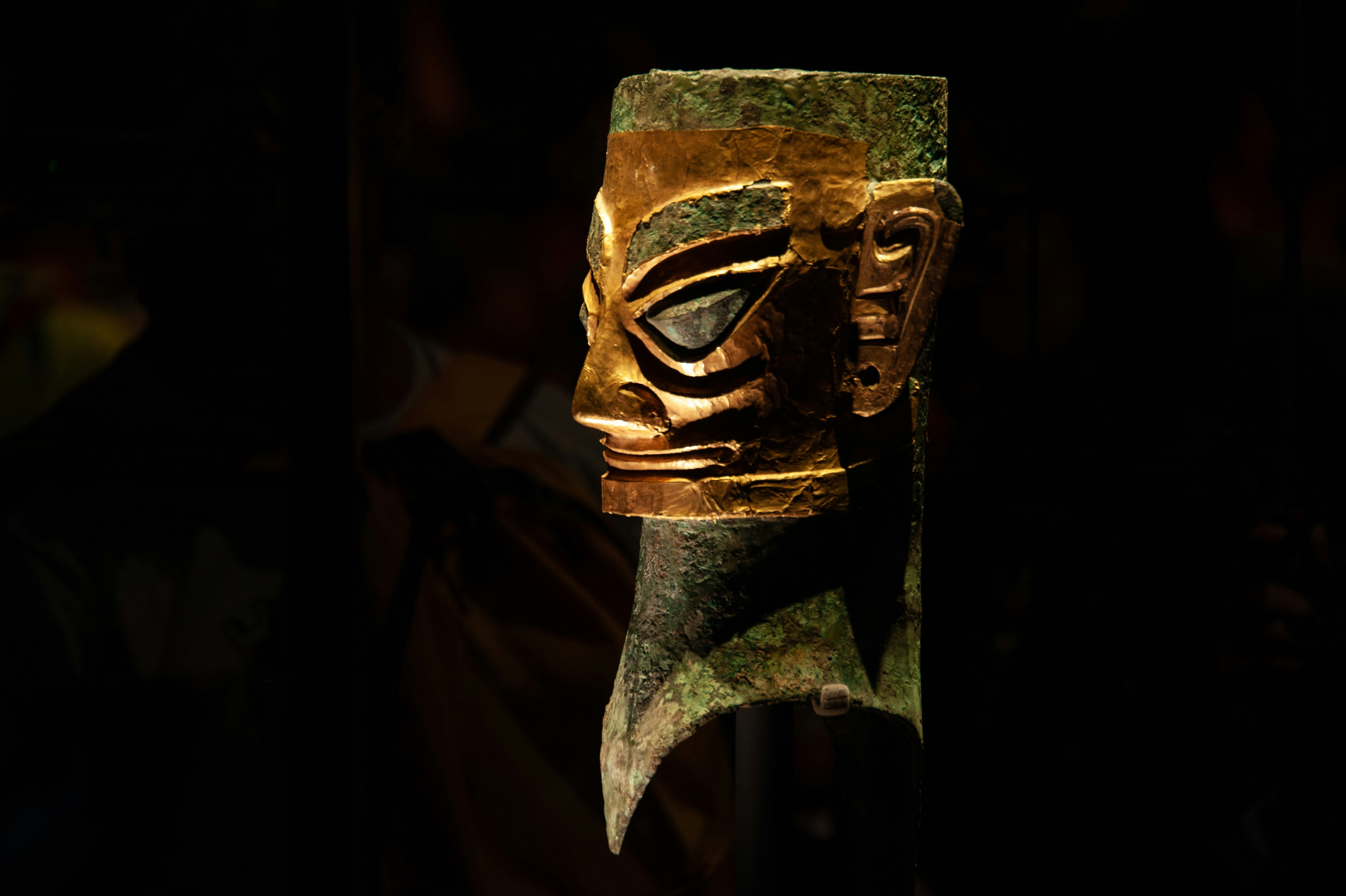 Intricately designed golden mask with green patina, showcasing ancient artistry and cultural significance.