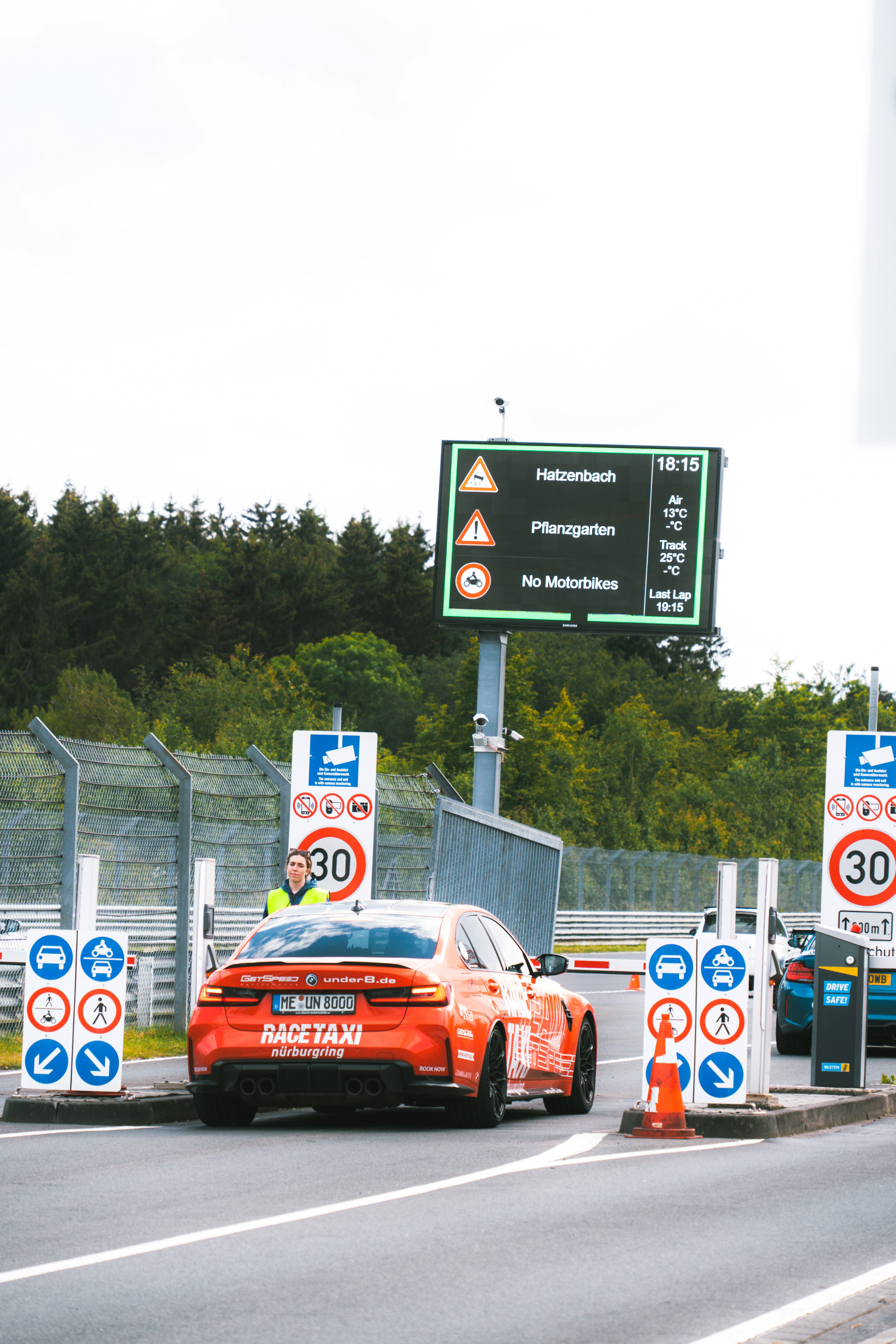 Red Race Taxi at the Pit Gate: Signage, Barriers, and a Forest Backdrop