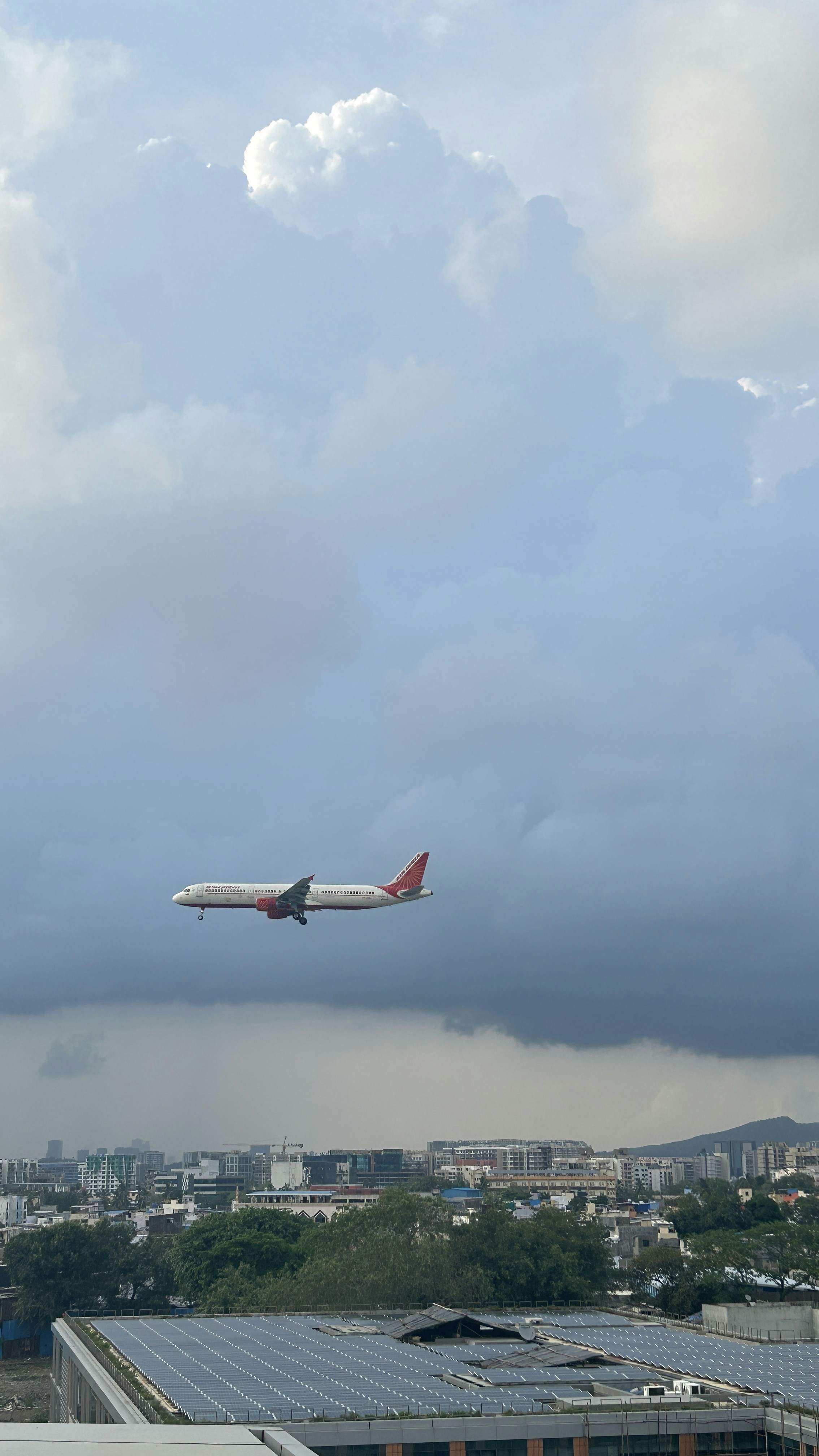 Commercial airplane gliding through a cloudy sky, nearing its landing in an urban landscape.
