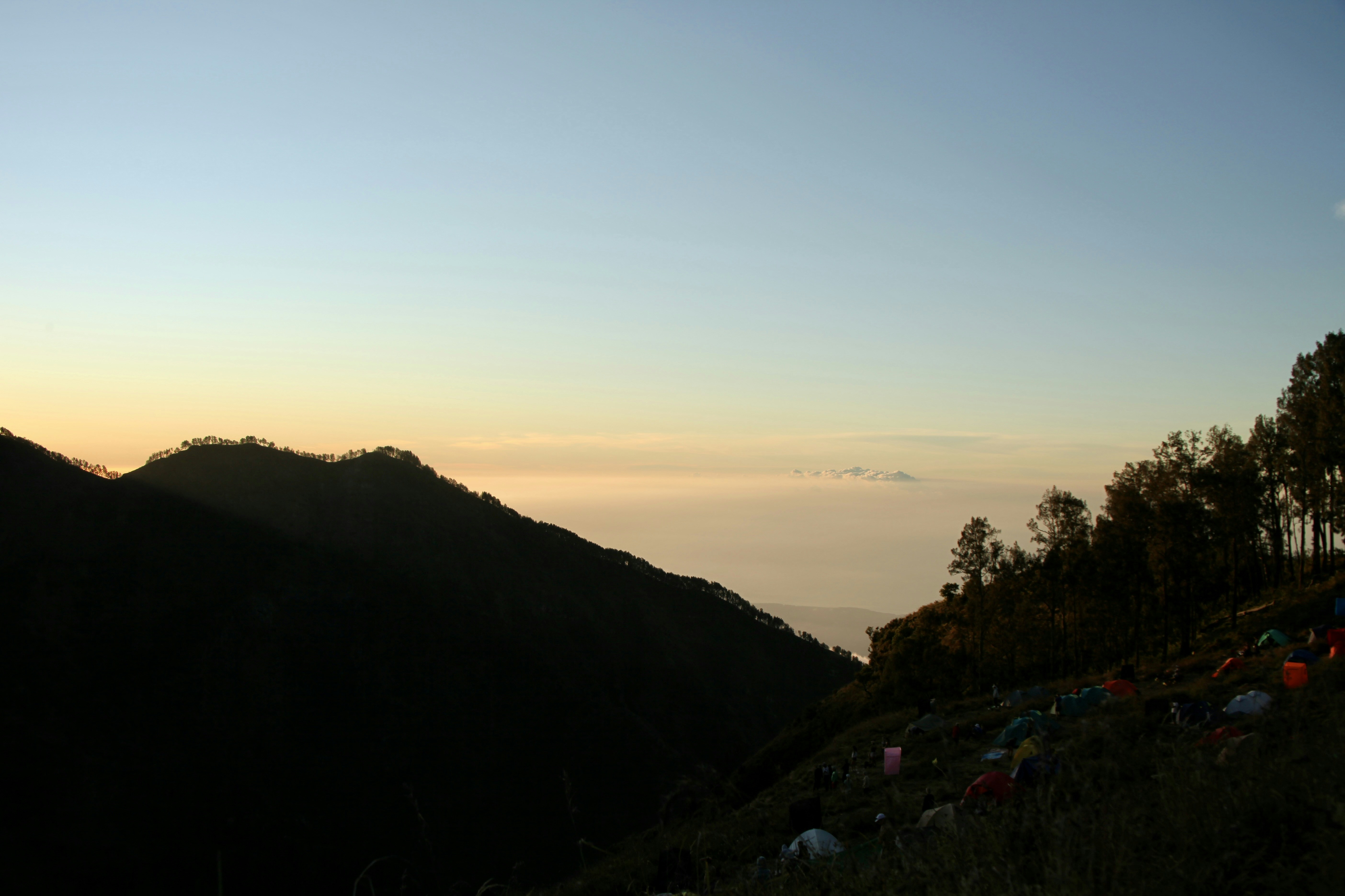 Silhouetted mountains and a hillside dotted with tents at sunrise.