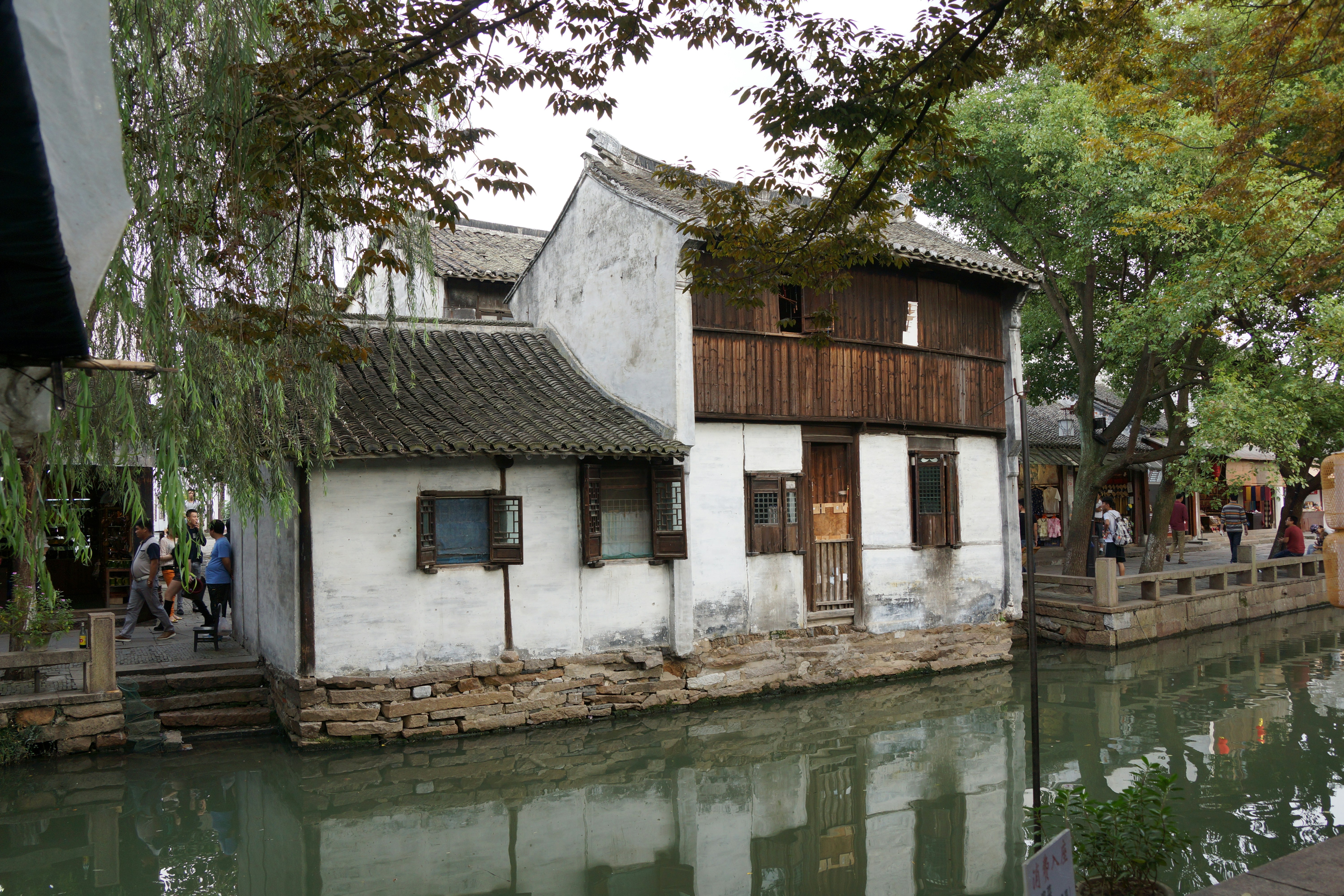 Traditional house with wooden accents by a tranquil canal, surrounded by lush trees.