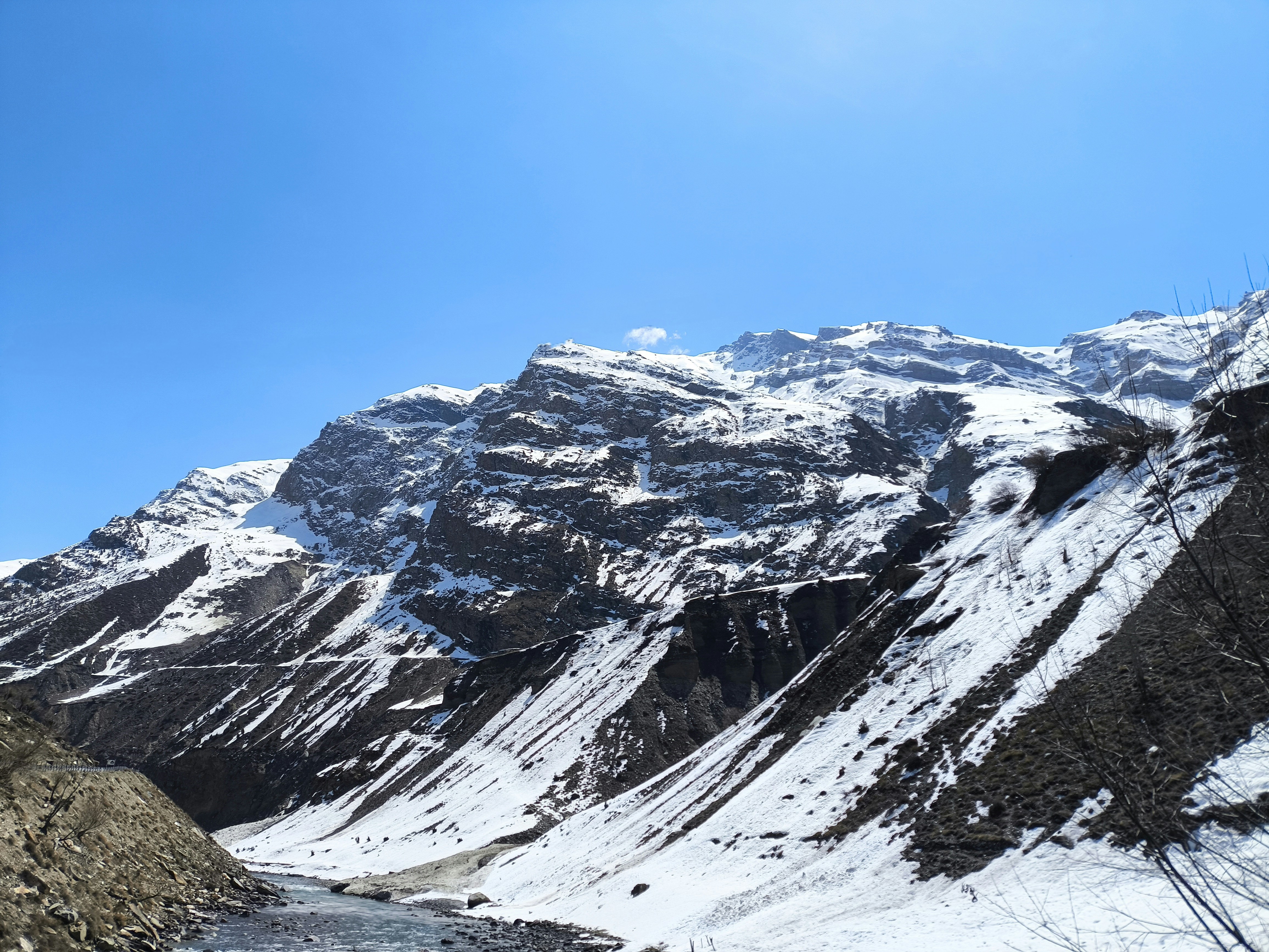 Snow-covered mountains under a vivid blue sky with a tranquil river winding through the valley.