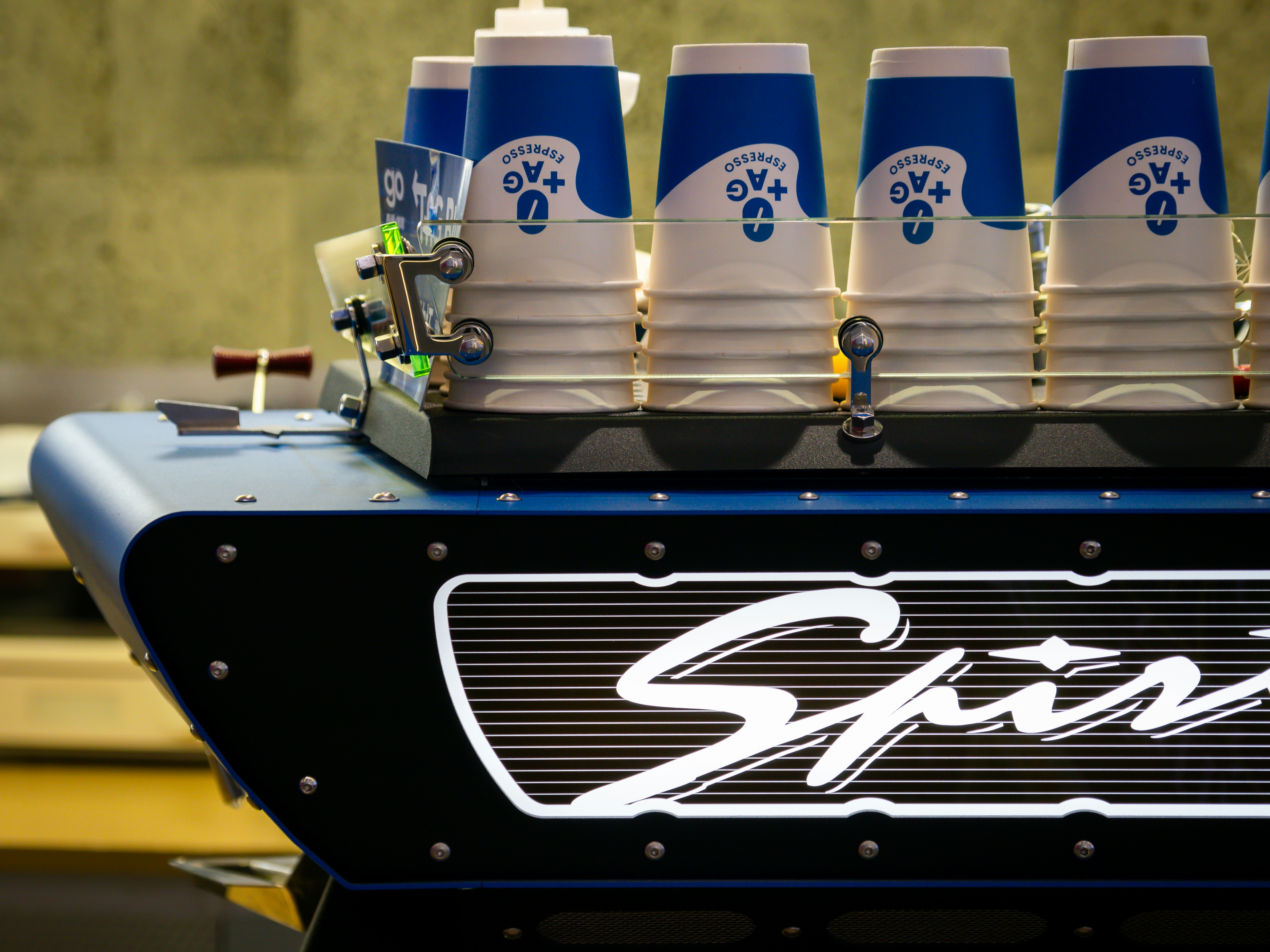 Close-up of a blue hull featuring a bold white script logo and a row of blue-and-white cups mounted along the edge. The image emphasizes branding, hardware fixtures, and nautical design cues.