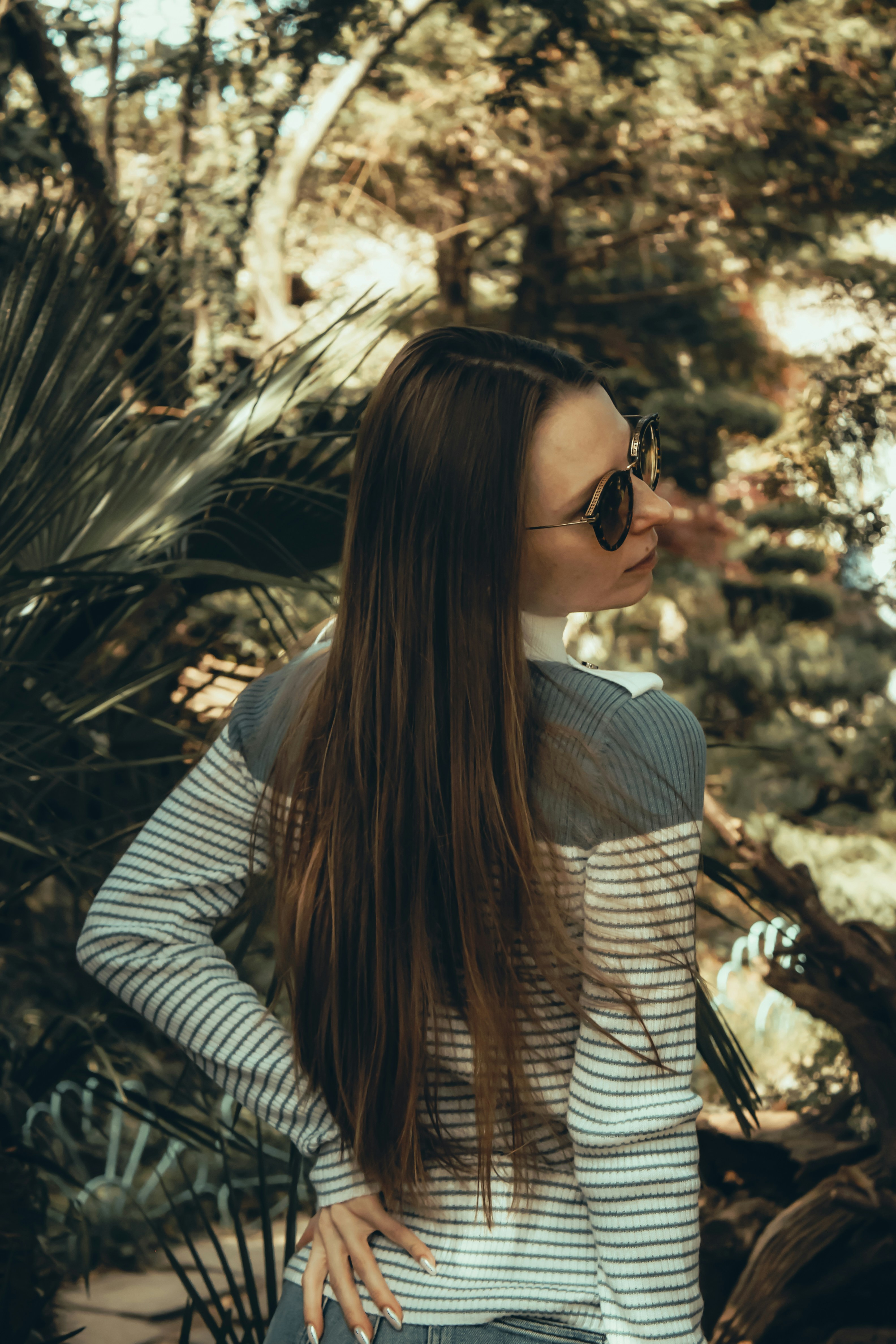 Woman in stylish attire poses amidst lush greenery, showcasing a blend of fashion and nature's tranquility.