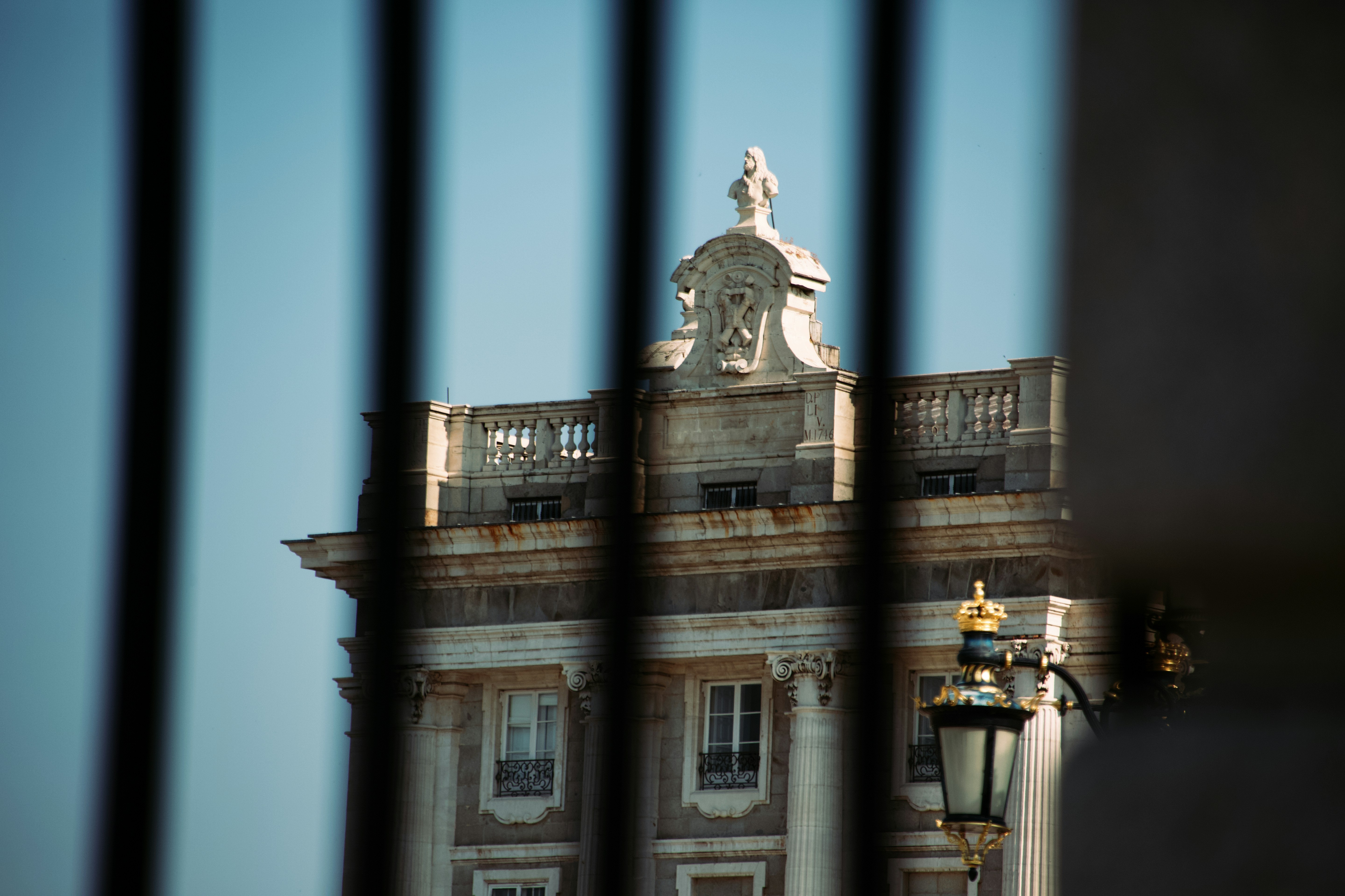 Historic building facade viewed through black iron bars under a clear blue sky.