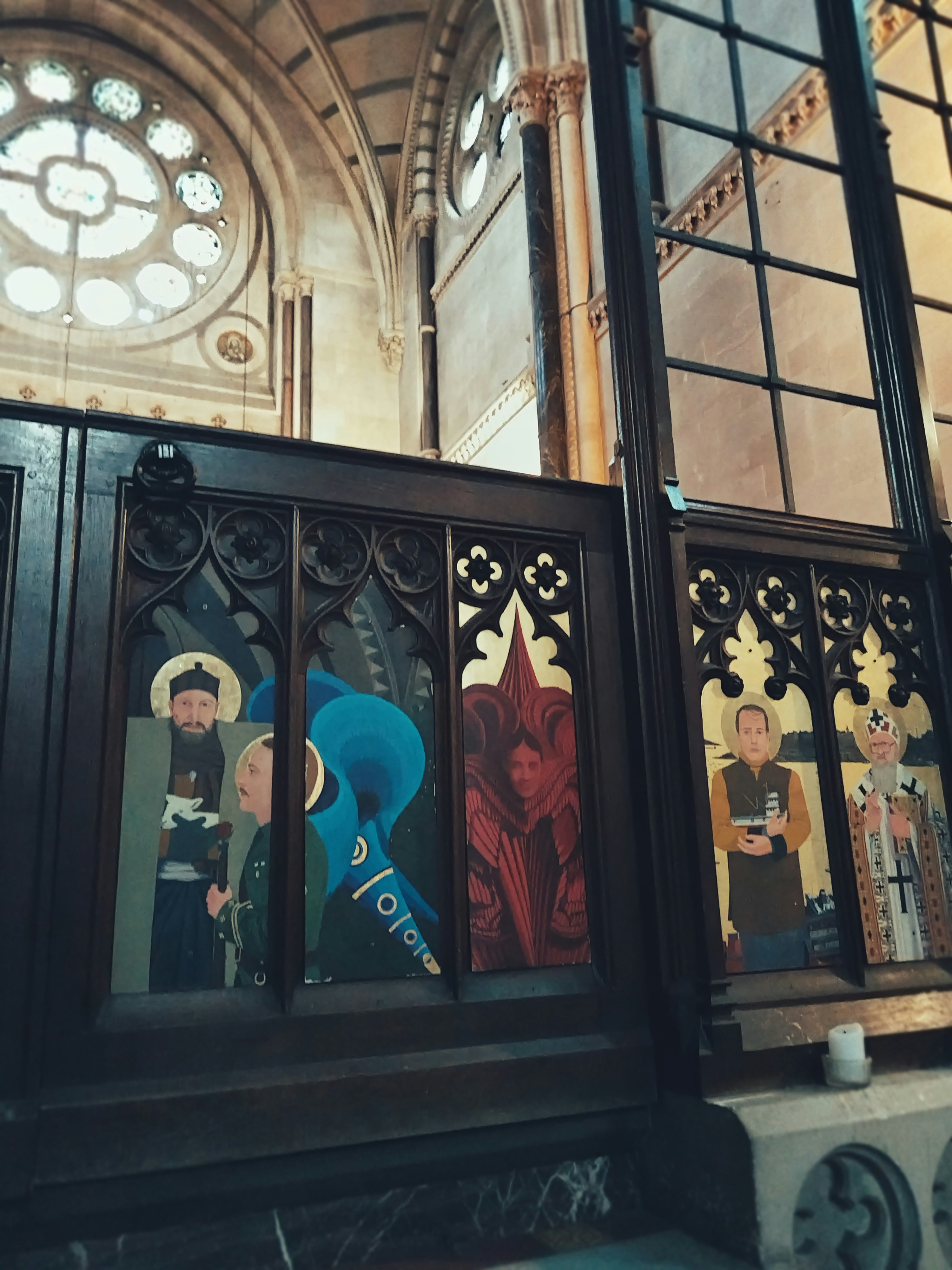 Vertical panel artwork inside a church, showcasing colorful illustrated figures behind dark decorative panels.