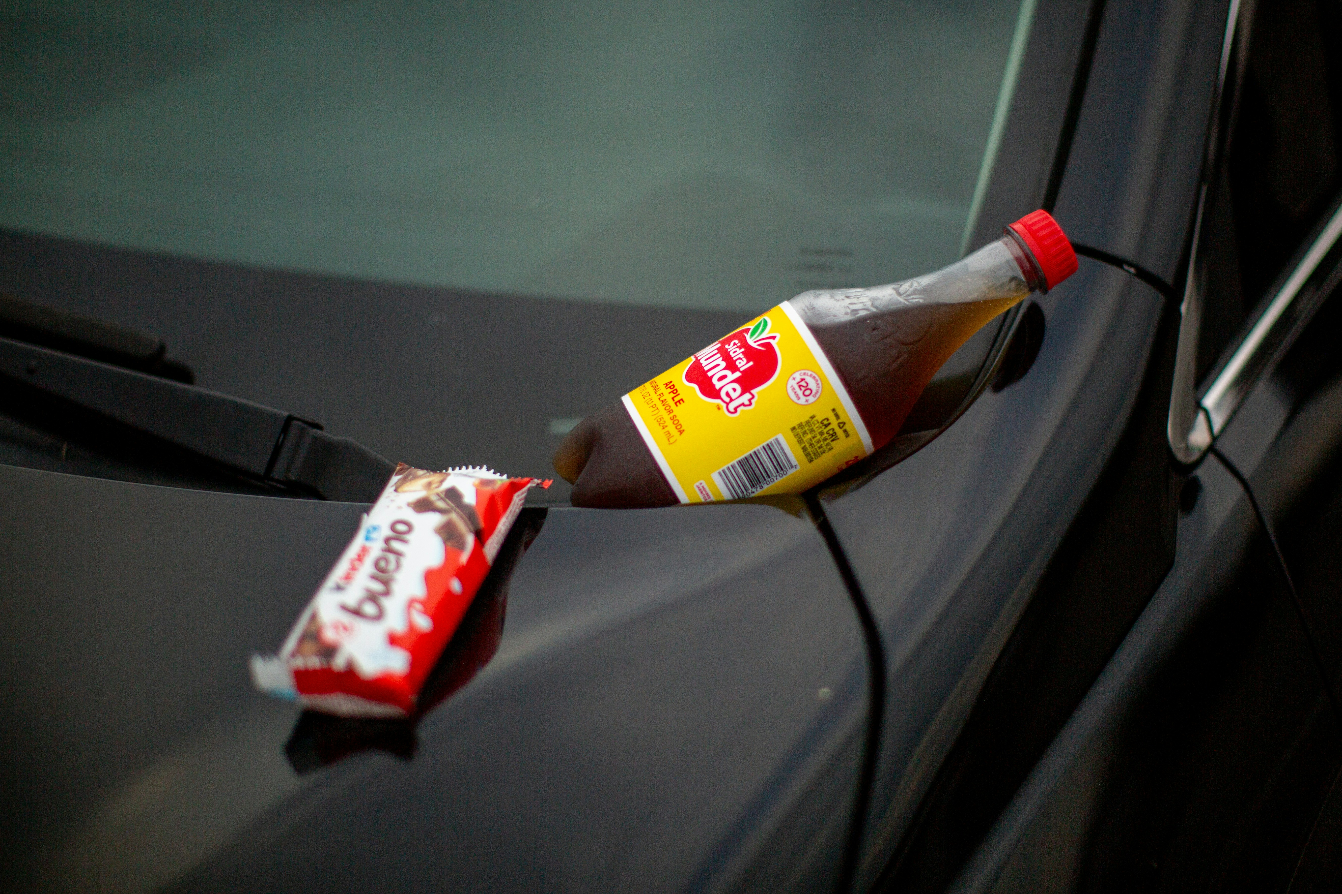 Red-Capped Bottle Pinned on a Glossy Car Hood
