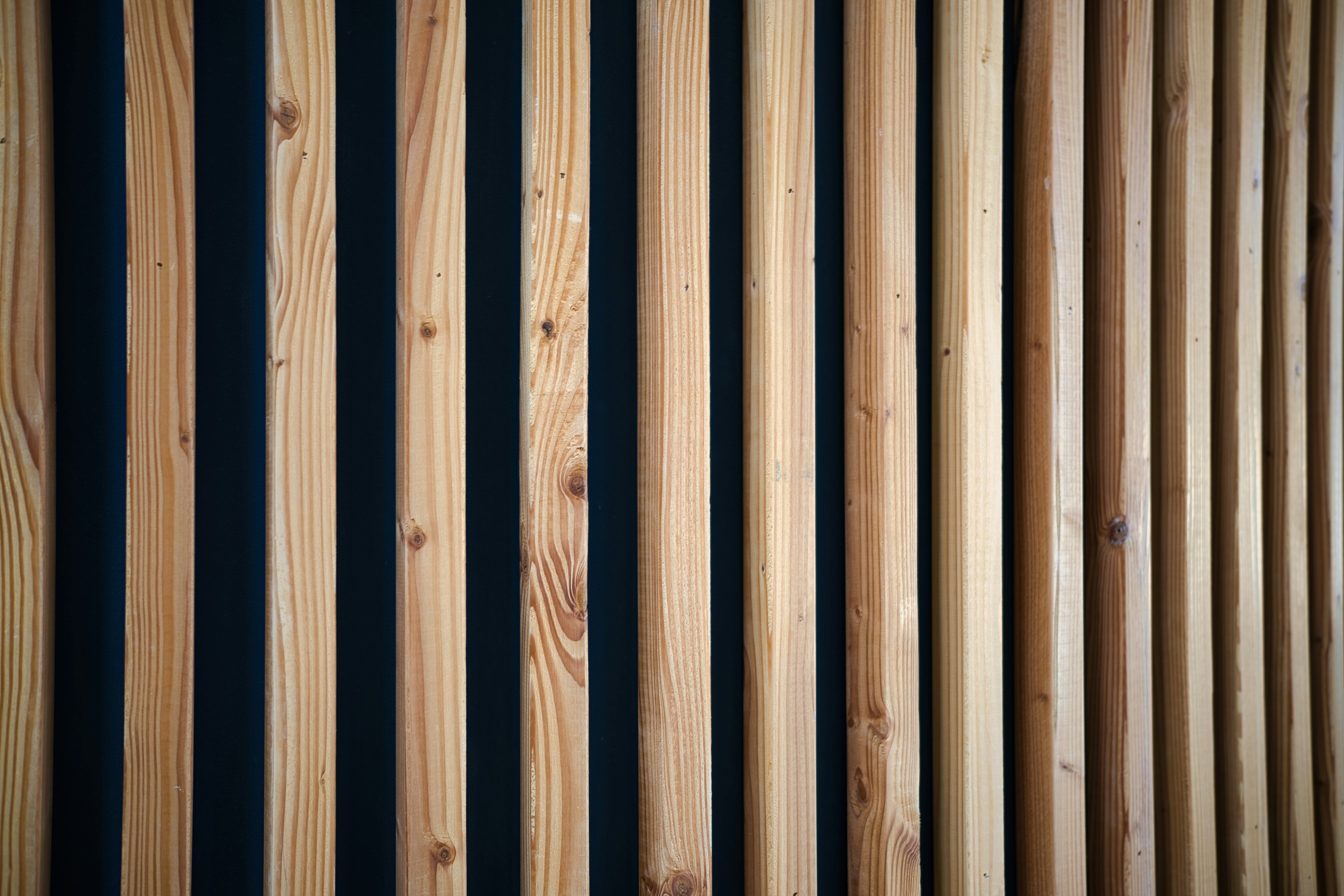 Photograph of closely spaced vertical wooden slats forming a striped pattern with alternating light and shadow.