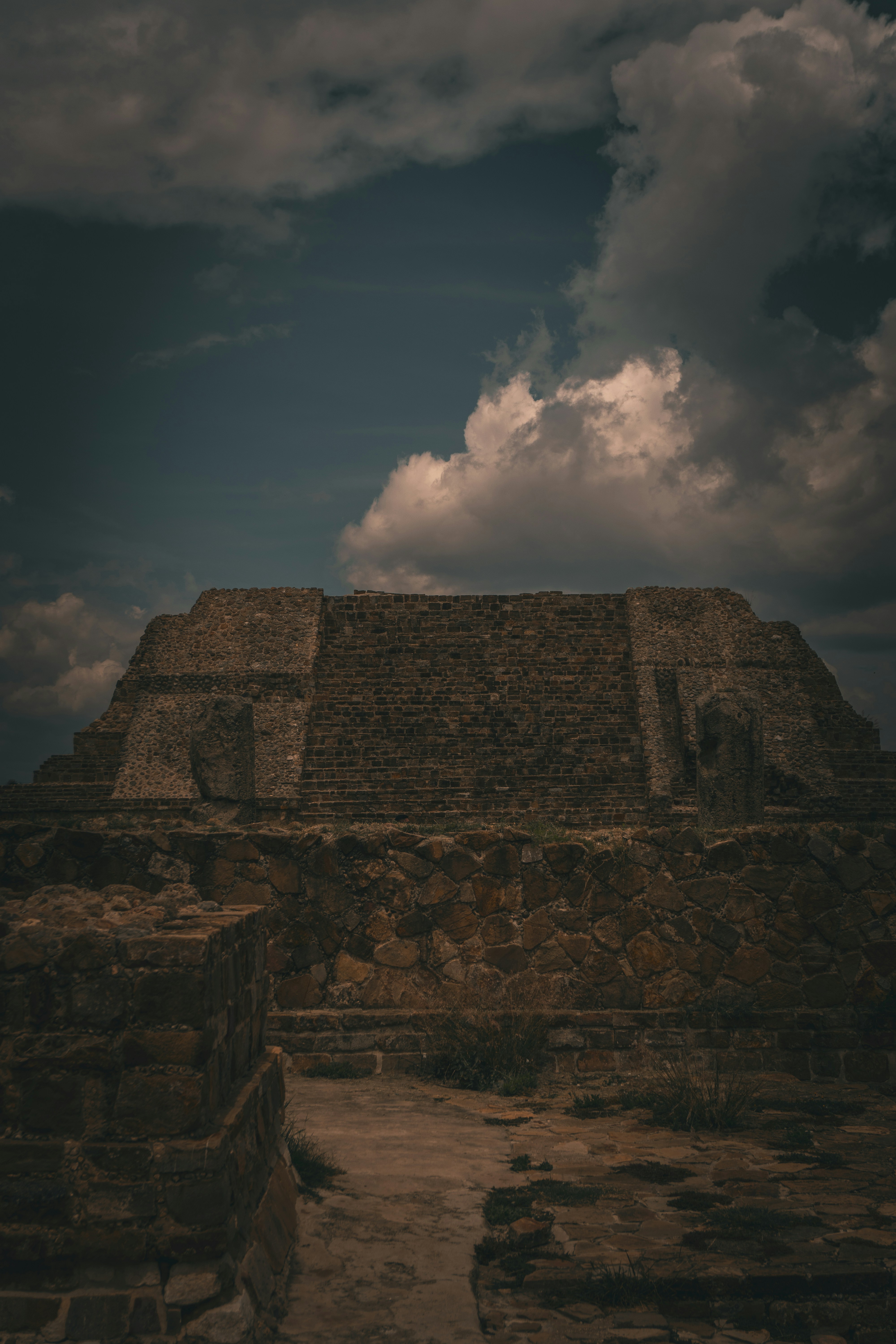 Stone pyramid with dramatic clouds gathering above in a moody sky.