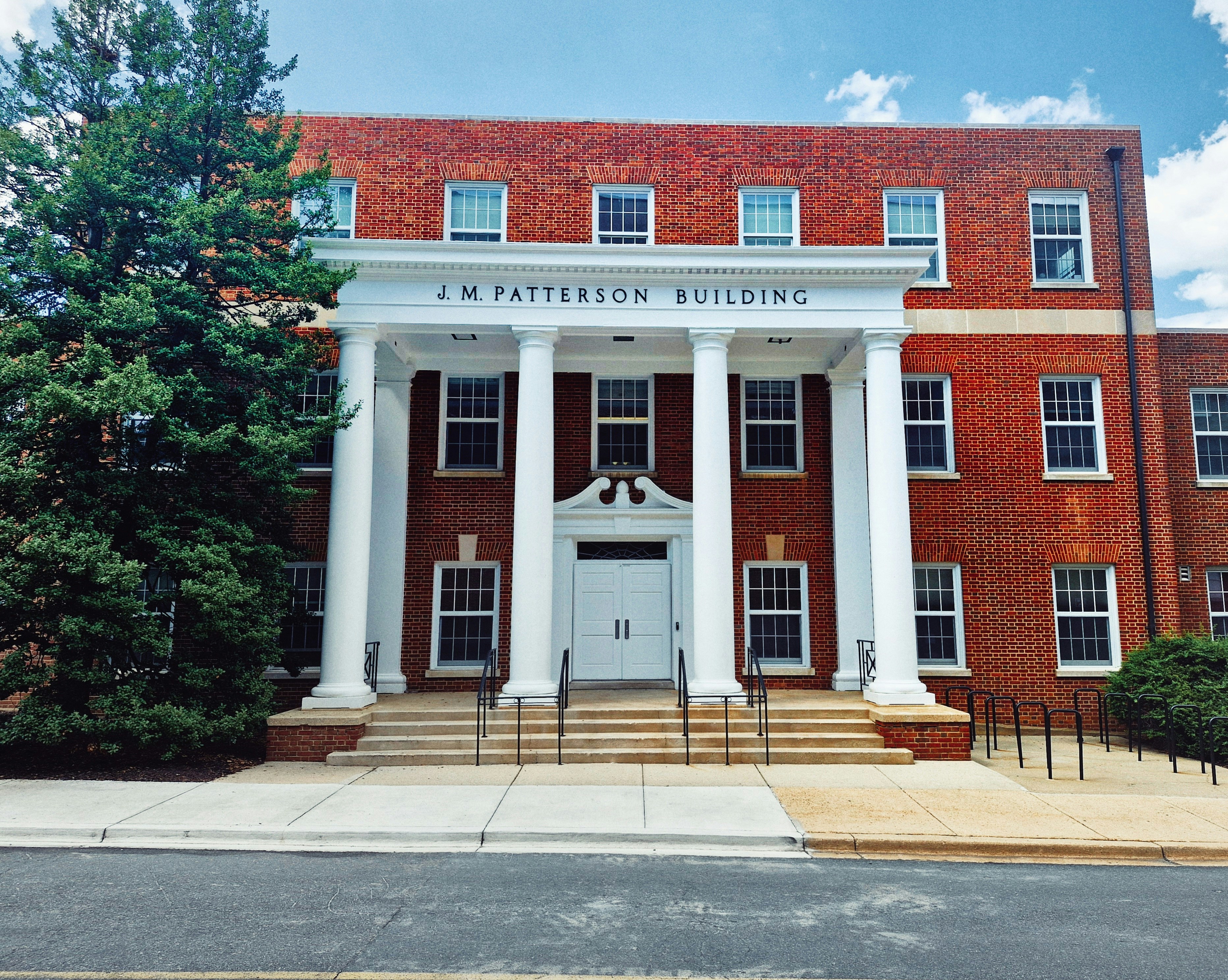 Red brick building with large white columns and symmetrical windows under a clear sky.