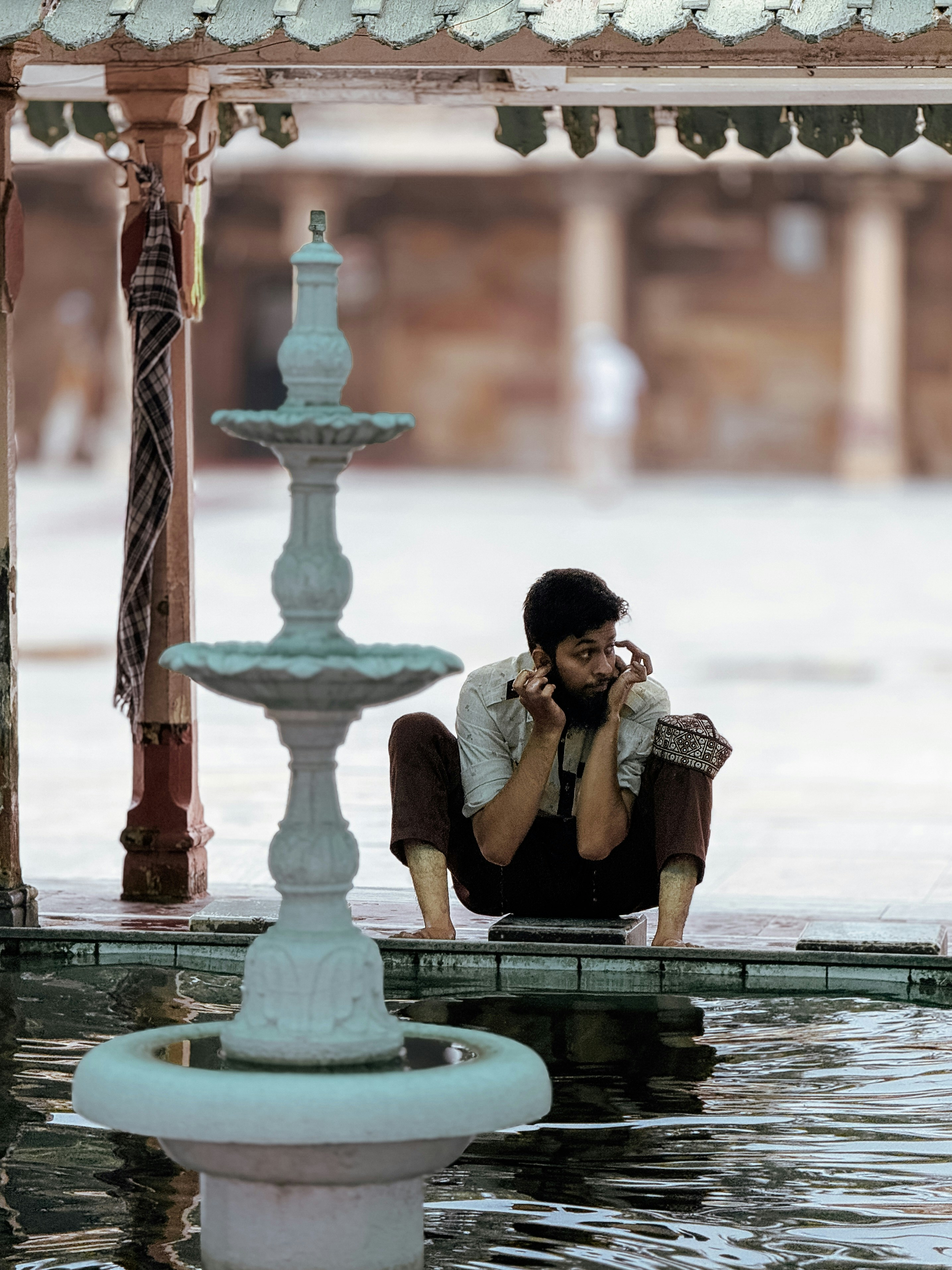 A man sitting on a fountain talking on a cell phone