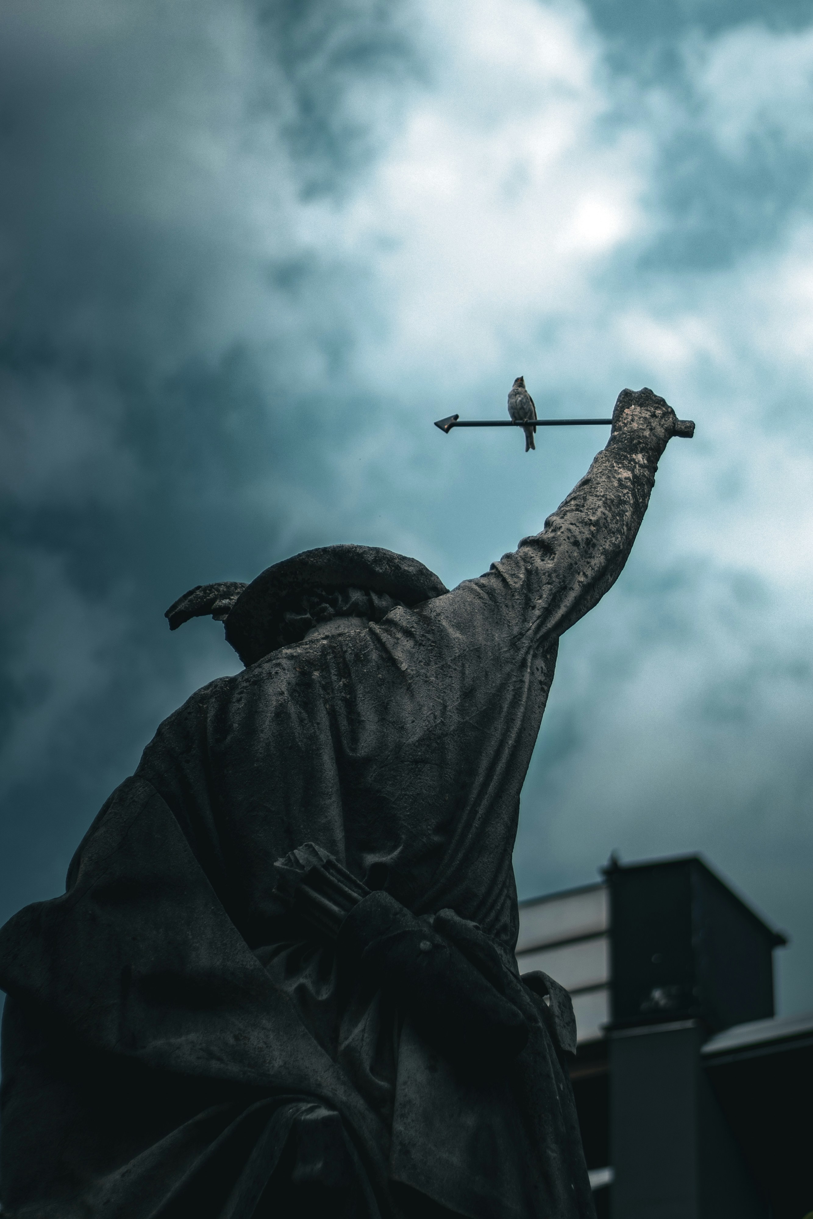 Sparrow on the weathered statue's rod beneath a moody sky