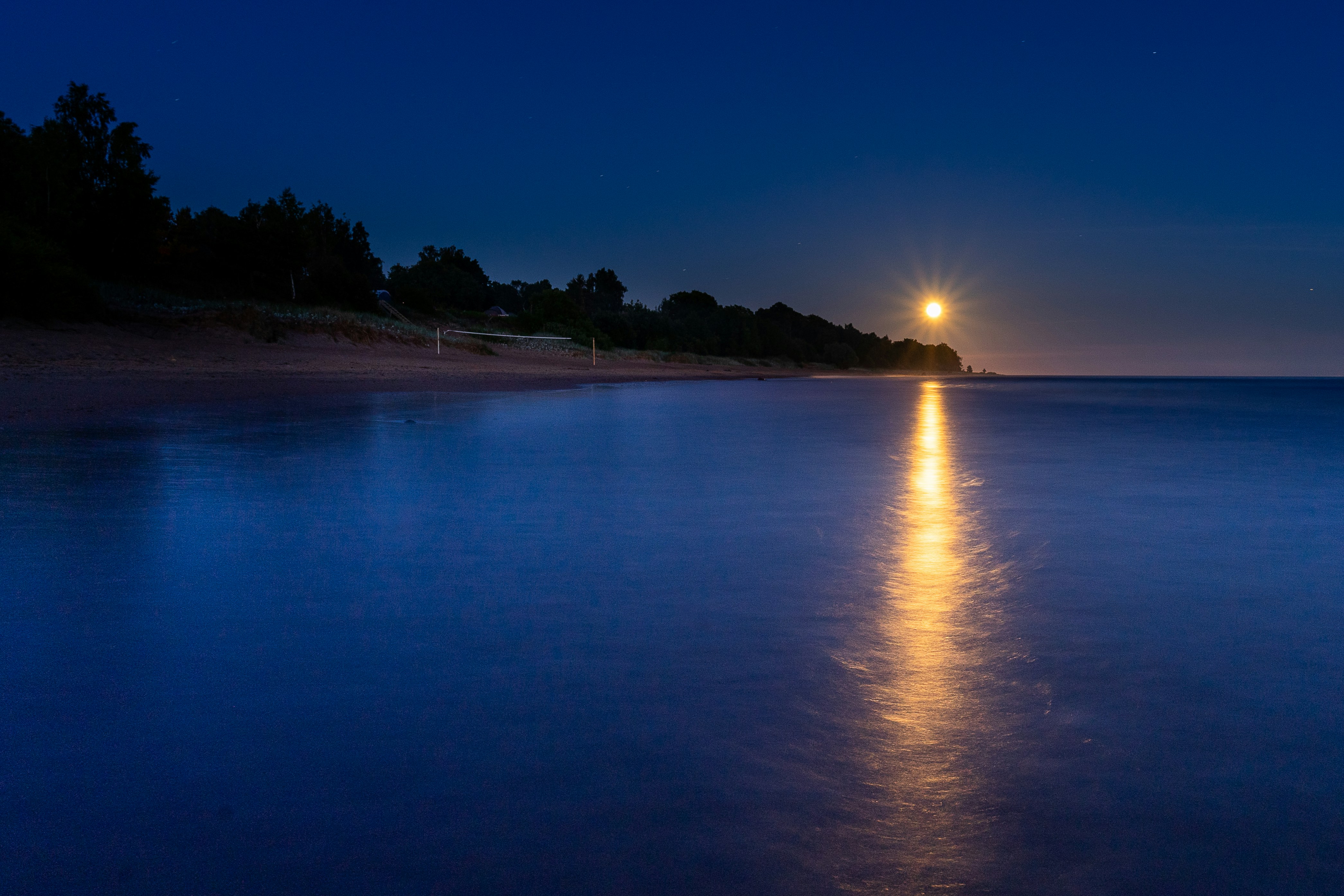 Moonlit shoreline: calm water and lighthouse glow