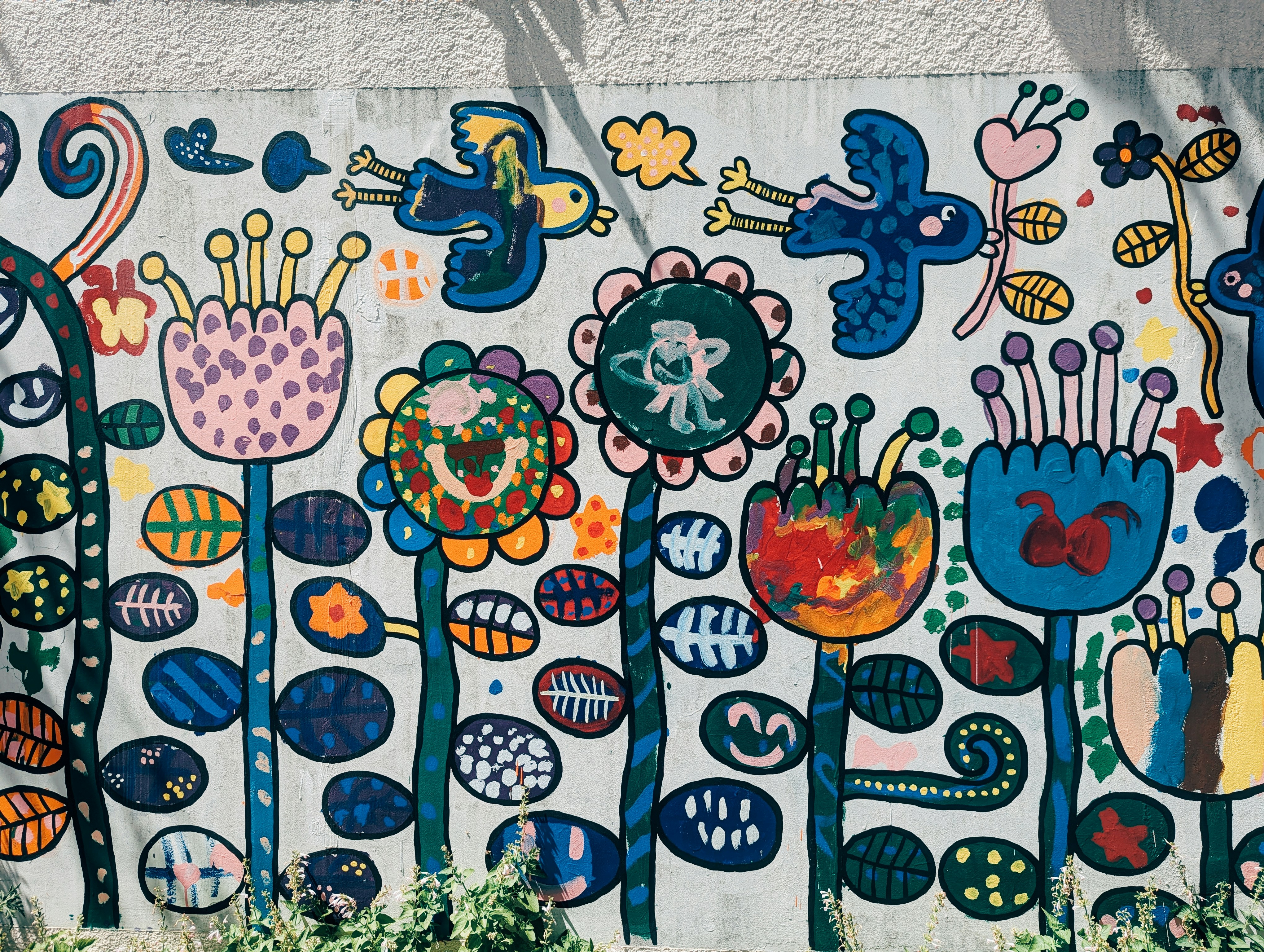 Vibrant mural featuring a variety of colorful flowers and playful birds, showcasing artistic expression in an urban setting.