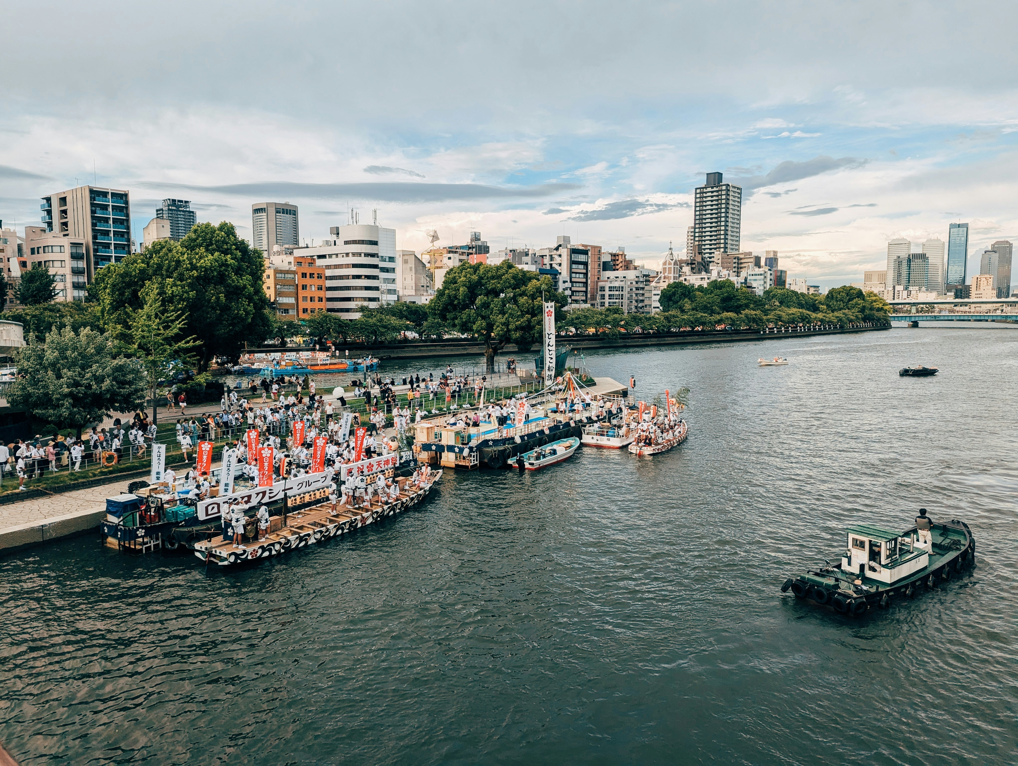 Photograph of a riverfront festival with colorful boats docked along the quay and a cityscape in the background.
