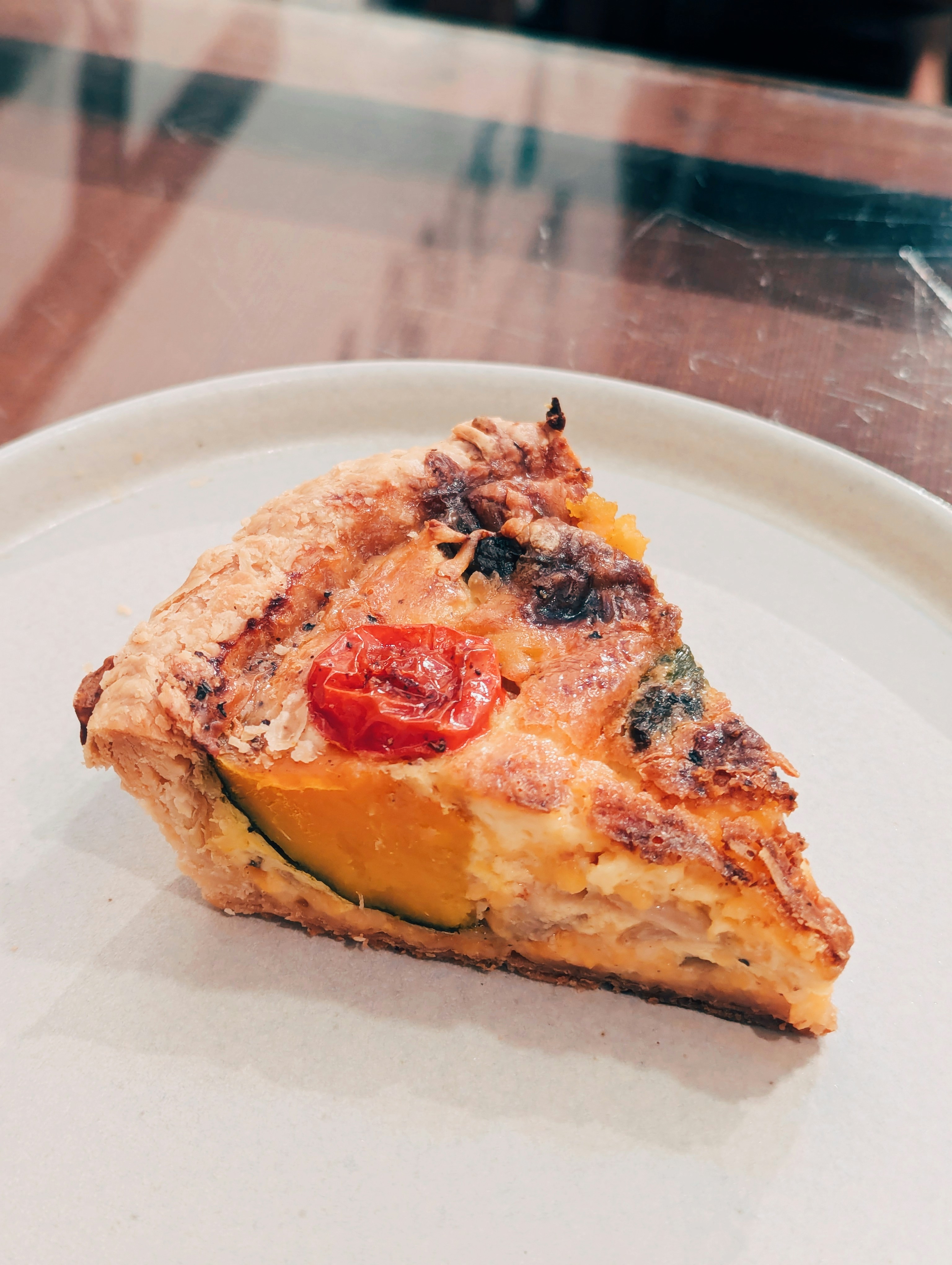 A slice of savory quiche featuring vibrant yellow squash and cherry tomatoes, resting on a simple plate.