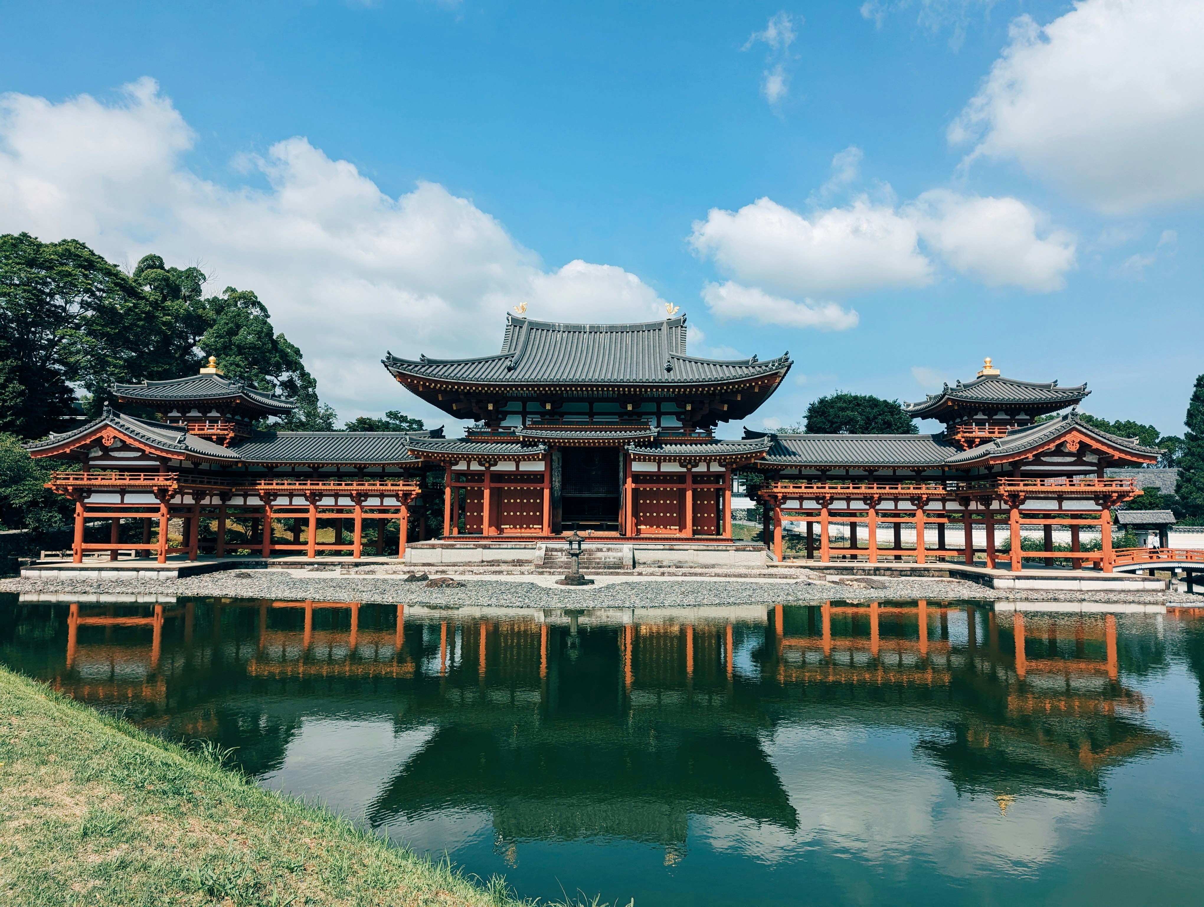 Traditional Japanese temple with ornate architecture reflected in a serene pond under a bright blue sky.