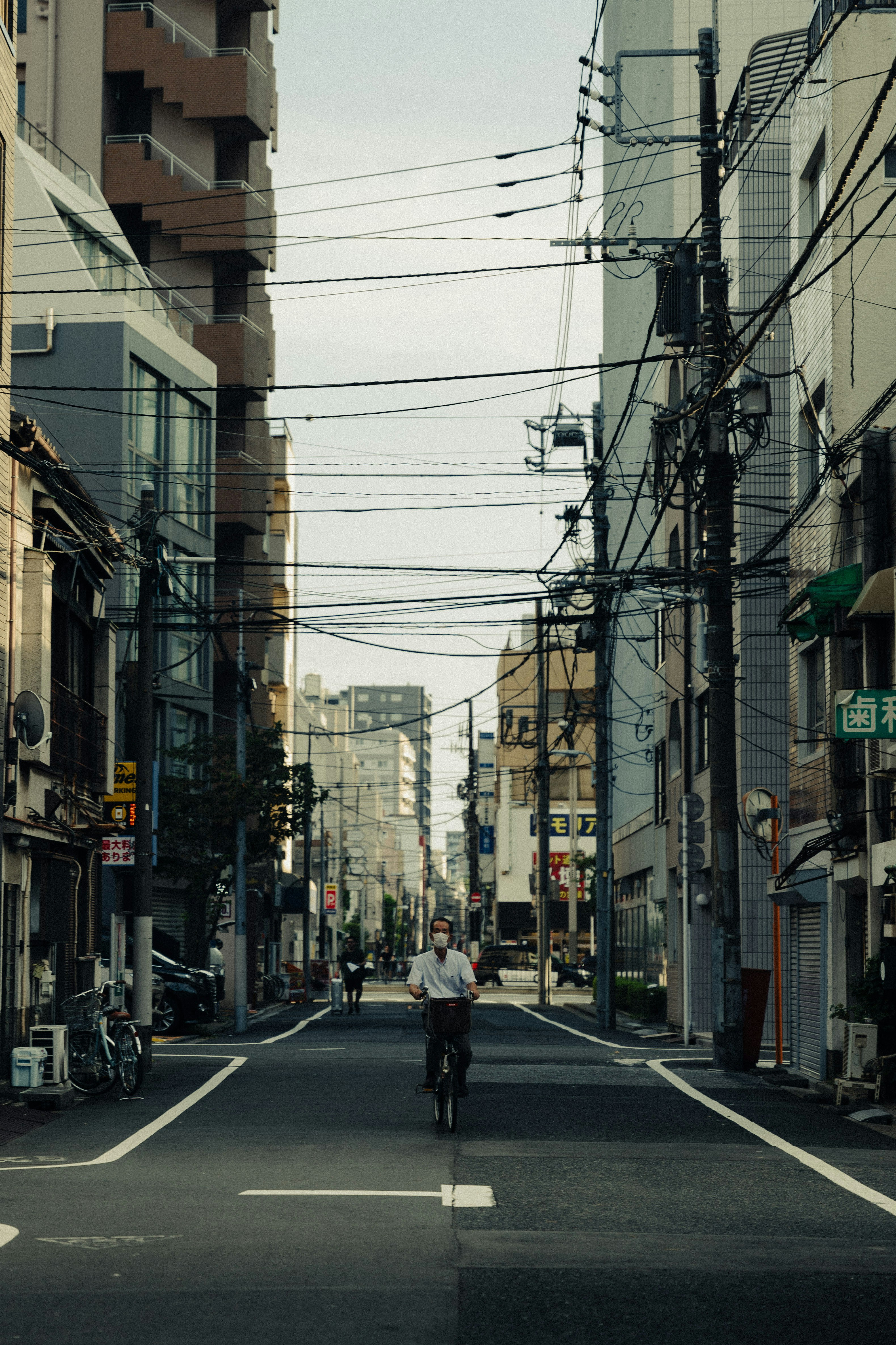 A cyclist navigates a quiet urban street lined with buildings and power lines, embodying the essence of city life. The scene captures a moment of tranquility amidst the bustling environment.
