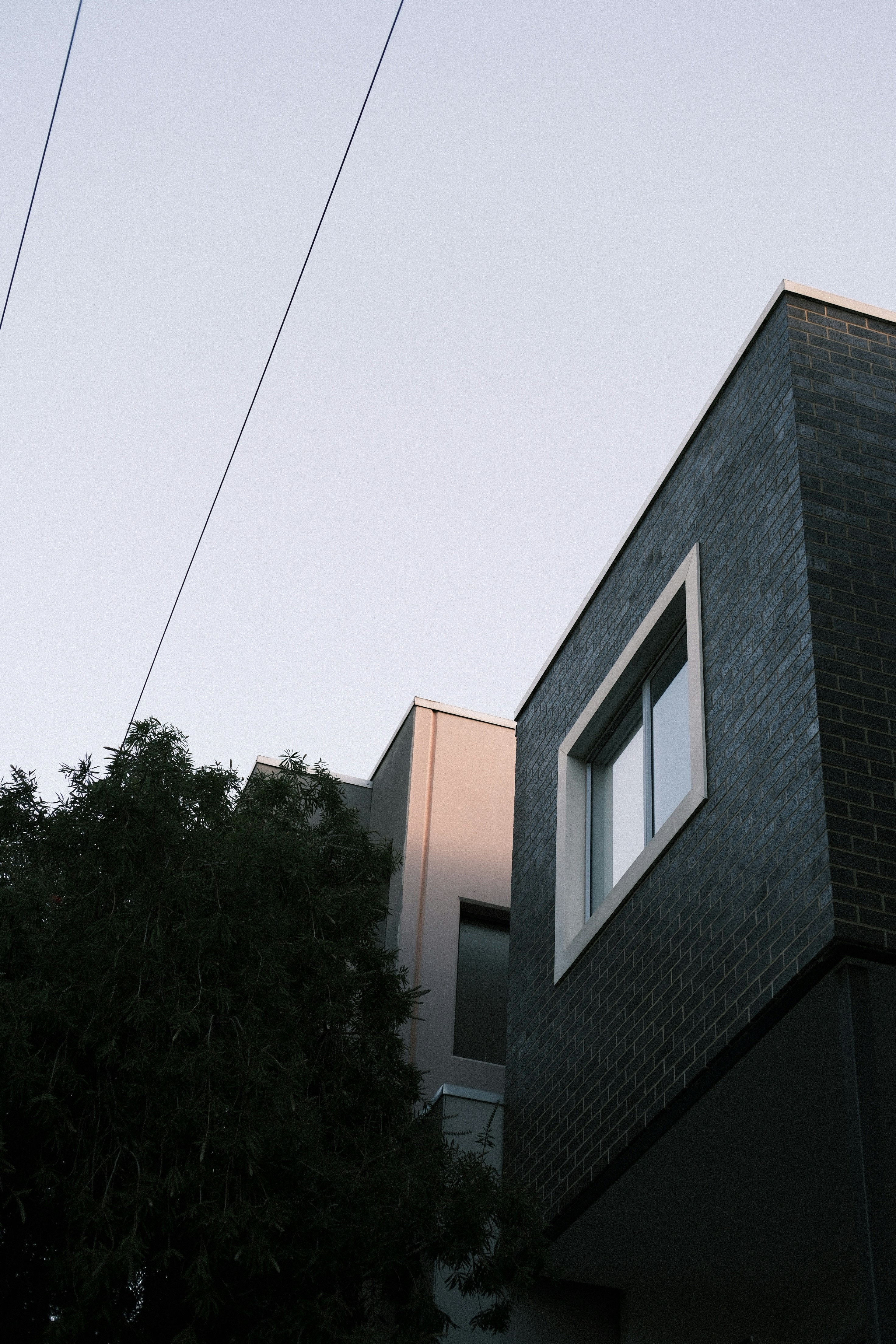 Sunlit Brick Corner Framed by Wires Against a Pale Sky