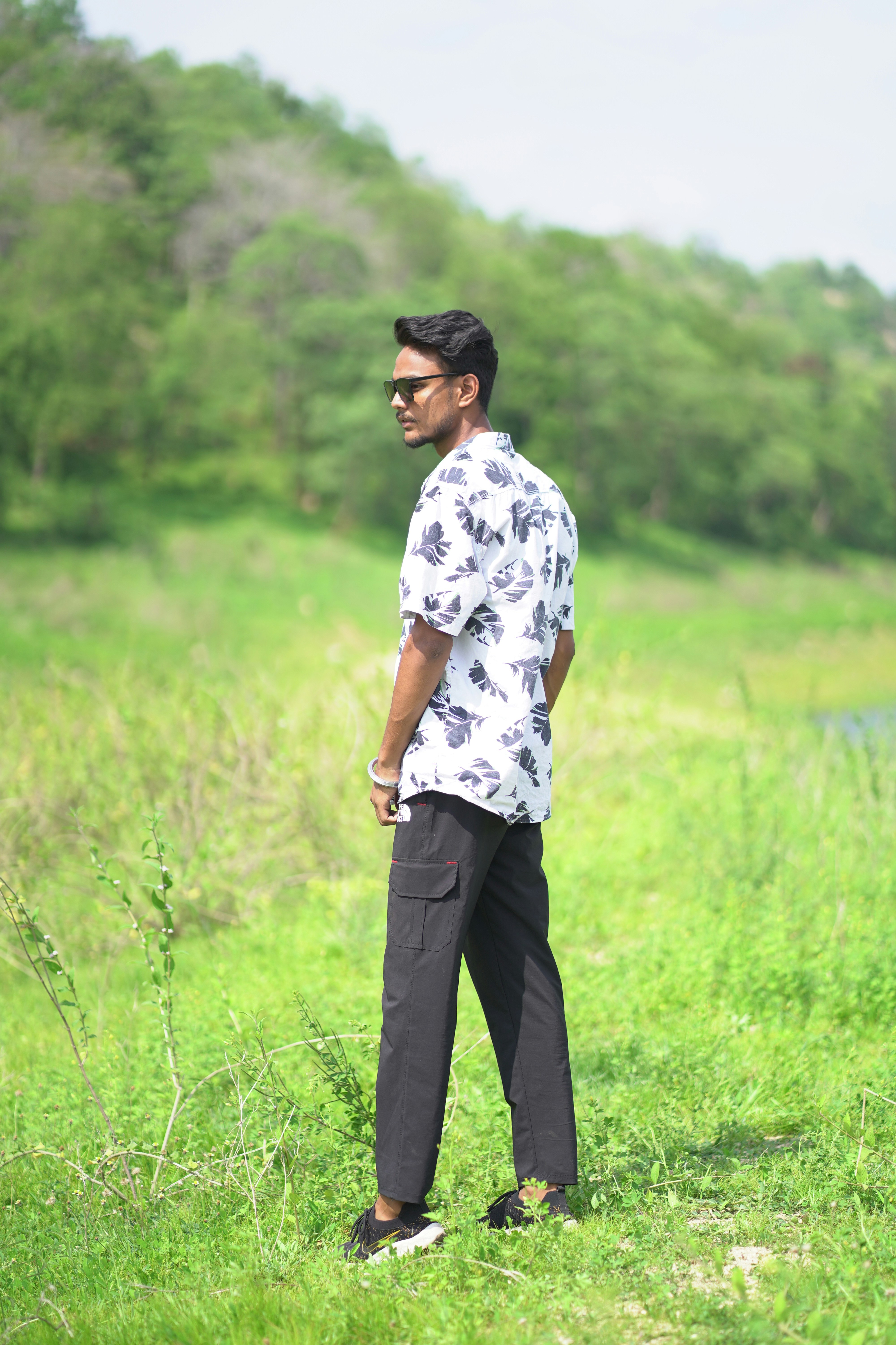 Man in a floral shirt stands in a lush green landscape, gazing into the distance. The scene captures a serene connection with nature.
