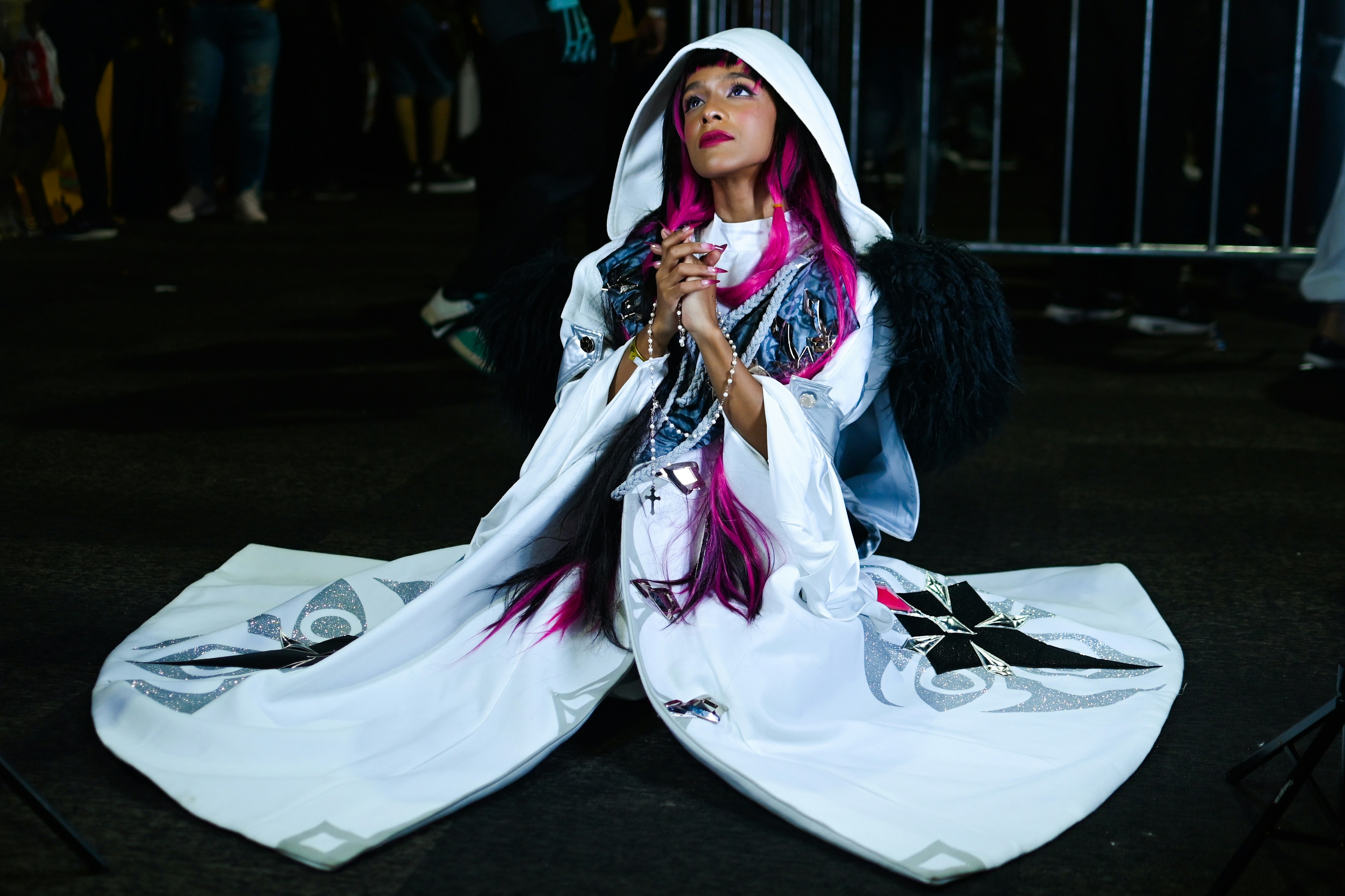 Neon Reverie: a magenta-haired figure in a flowing white cloak kneels on a dim stage