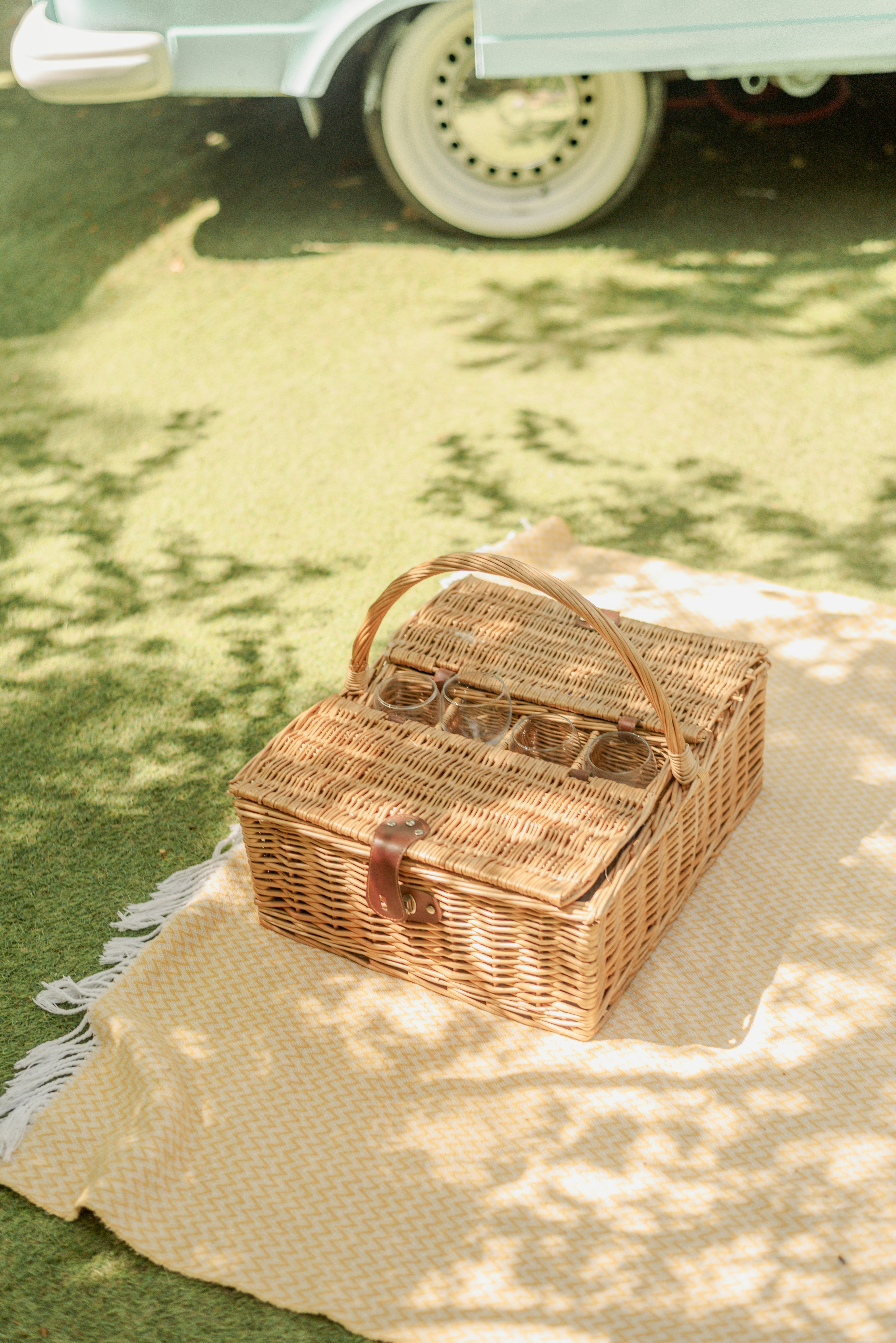 Woven picnic basket resting on a yellow checkered blanket, surrounded by soft grass and dappled sunlight.