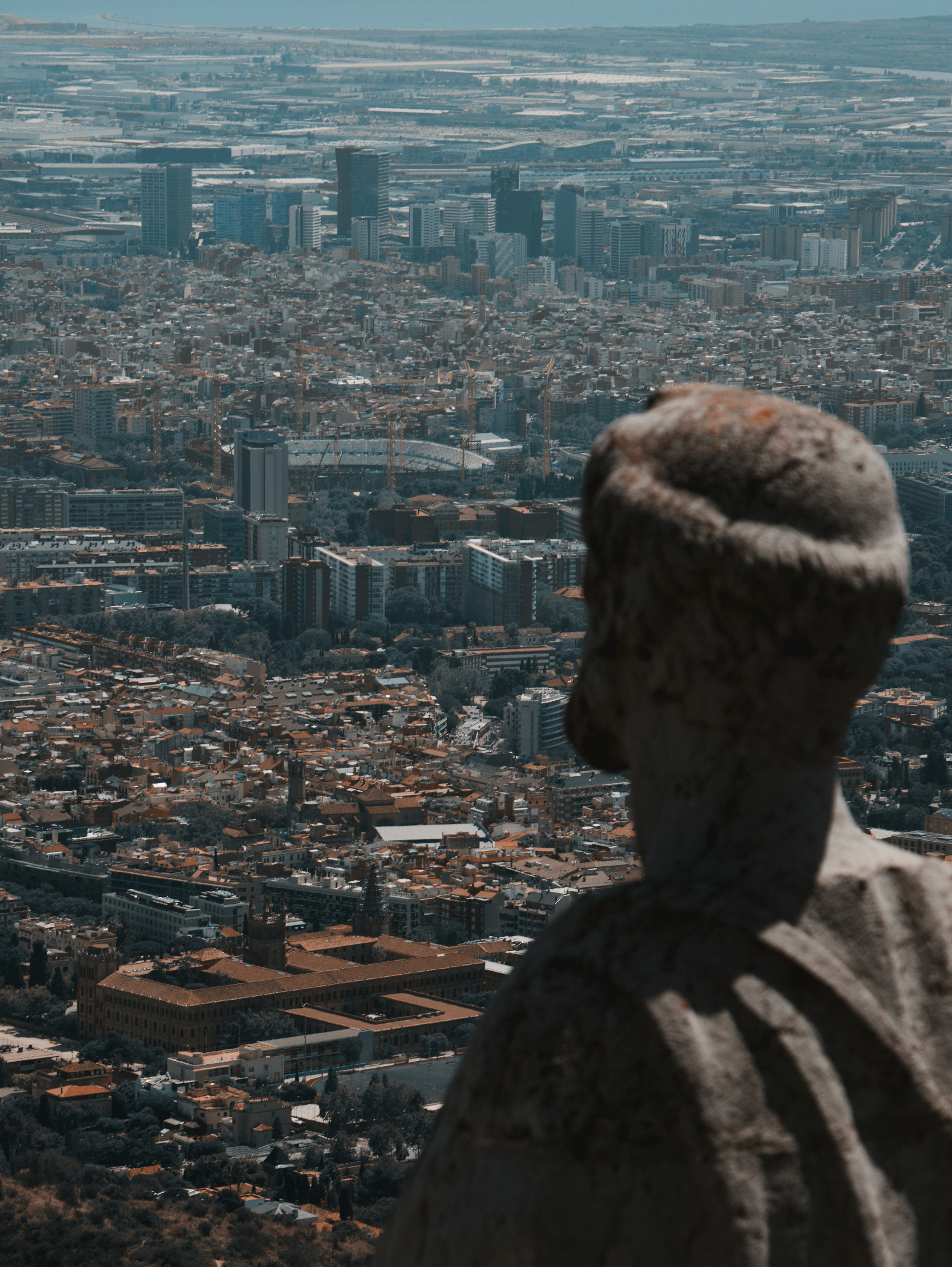 Overlooked City: A Weathered Statue Gazes Toward the Urban Span