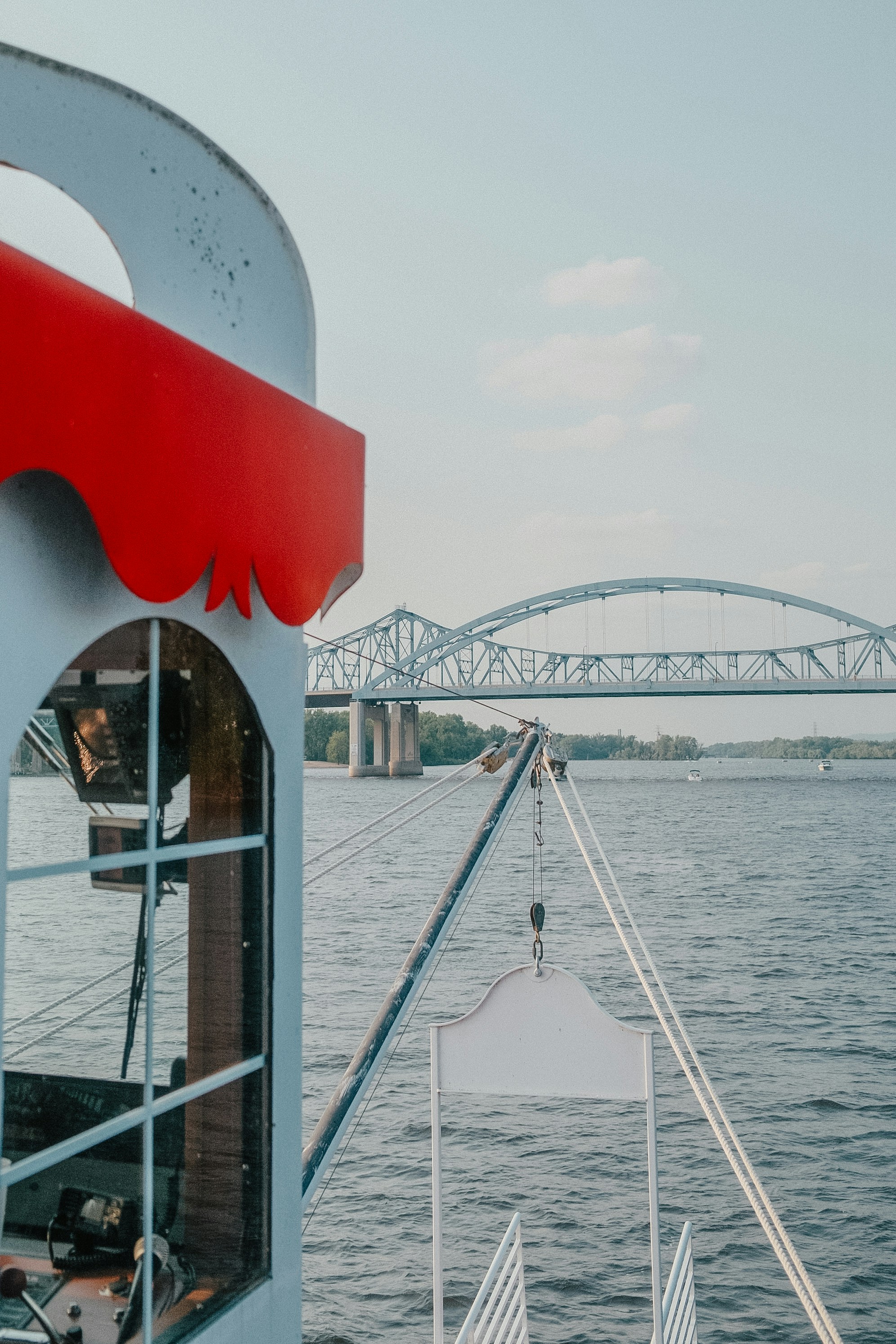 A red and white boat on water with a bridge in the background