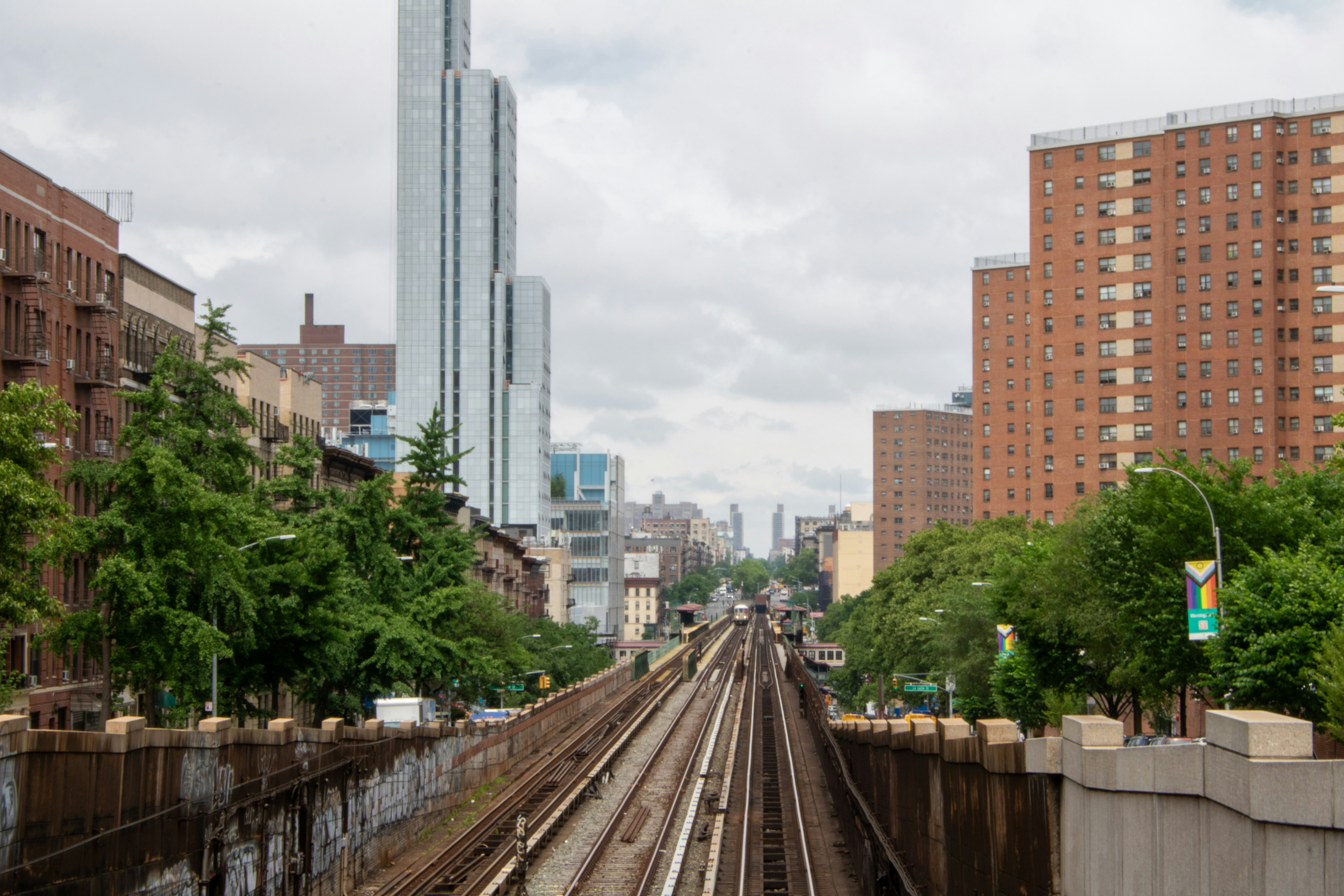 Rail tracks stretch into the distance with towering buildings lining the view on a cloudy day.