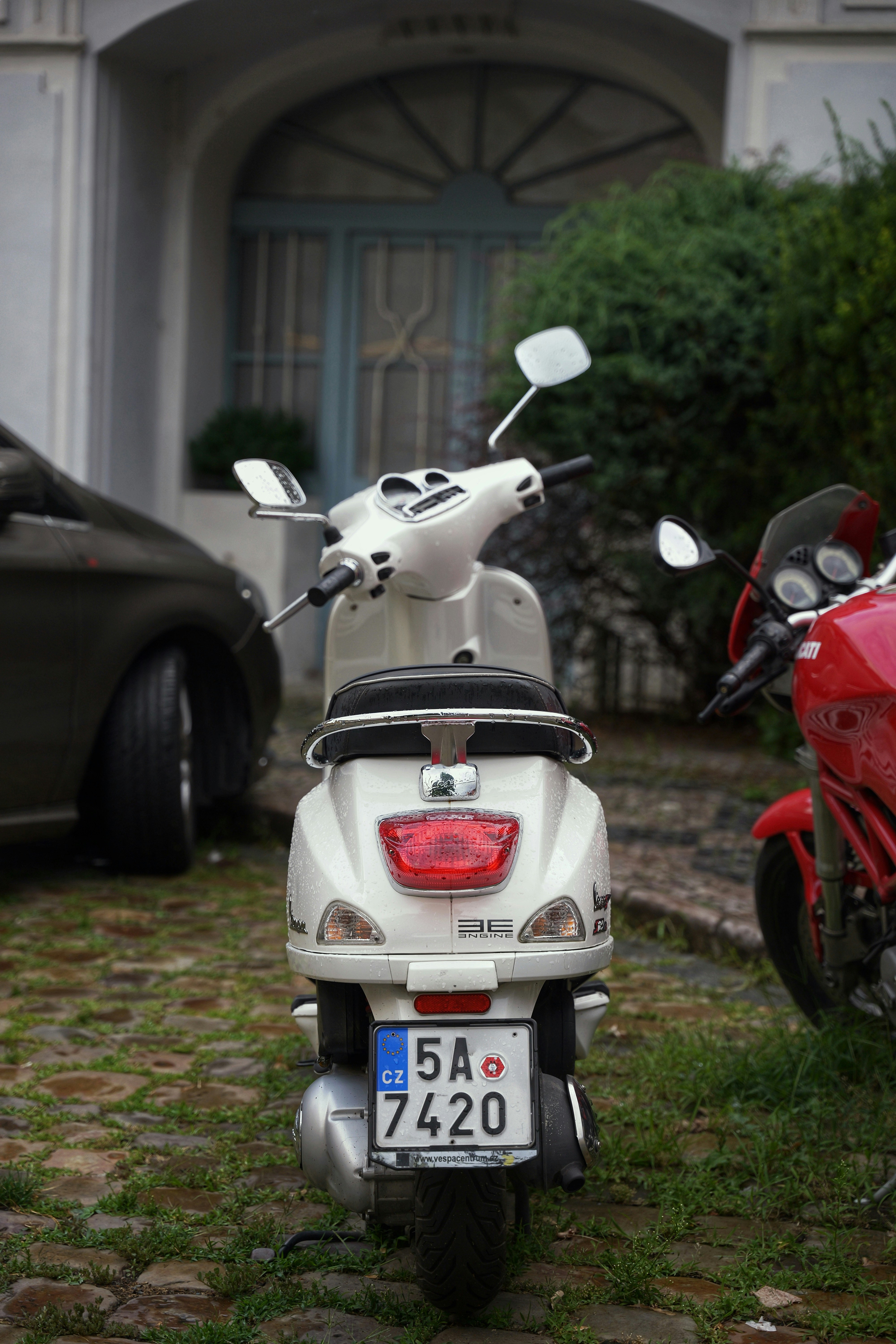 Cobblestone Quiet: White Vespa Framed Between Cars