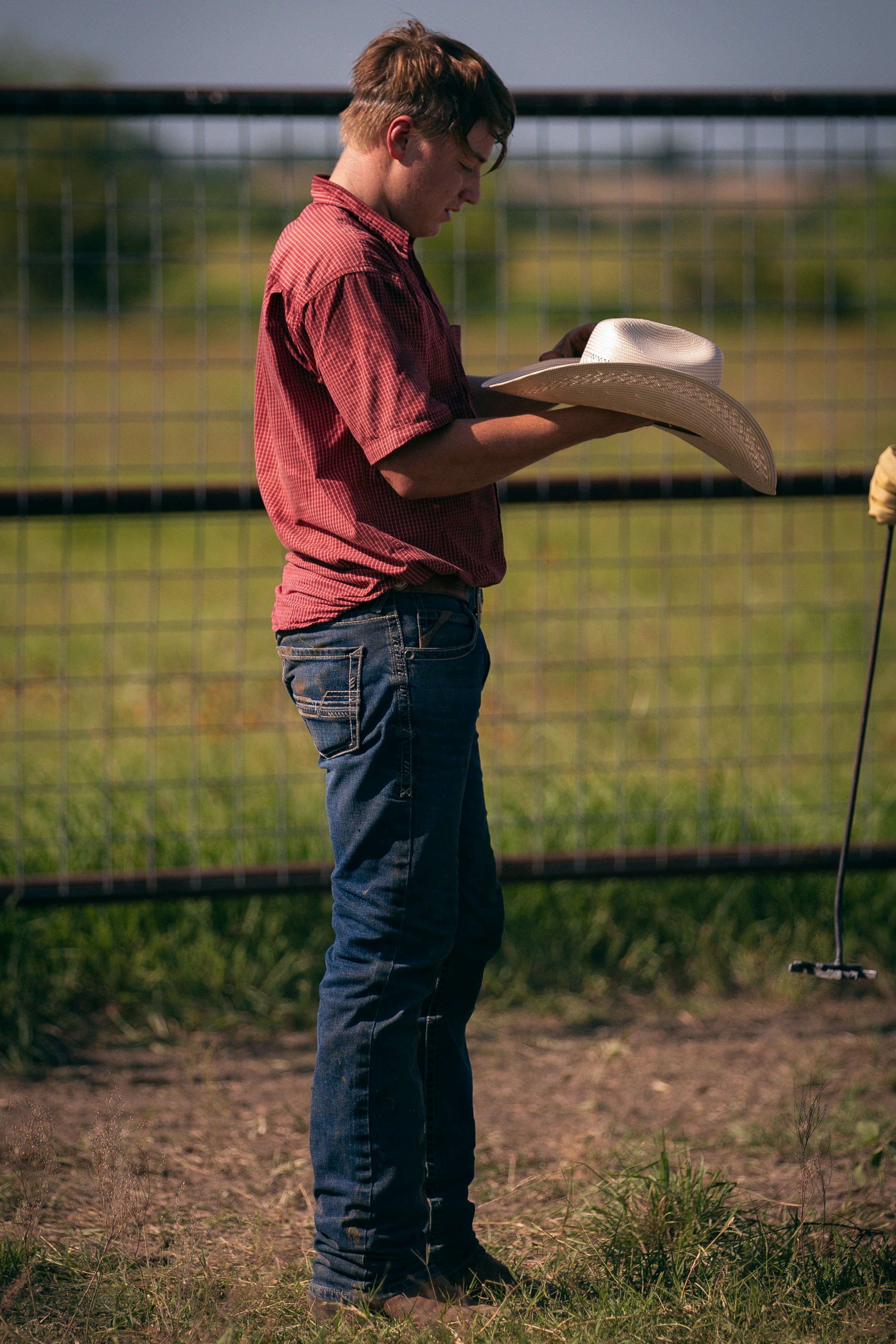 Red Shirt, Quiet Ritual: A Cowboy Hat Pause by the Fence