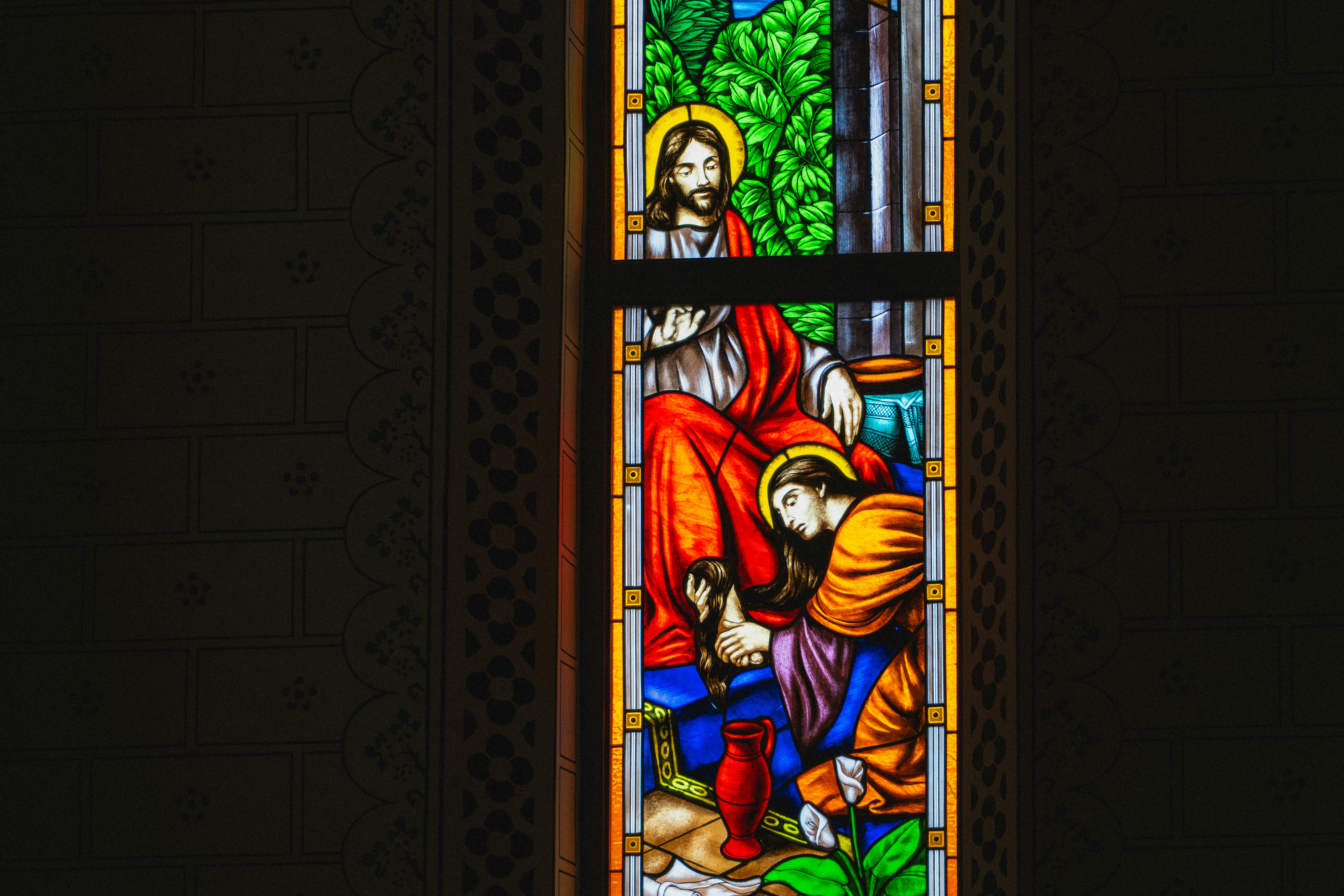 Vibrant stained glass window depicting a biblical scene with vivid greens and reds against a dark background.