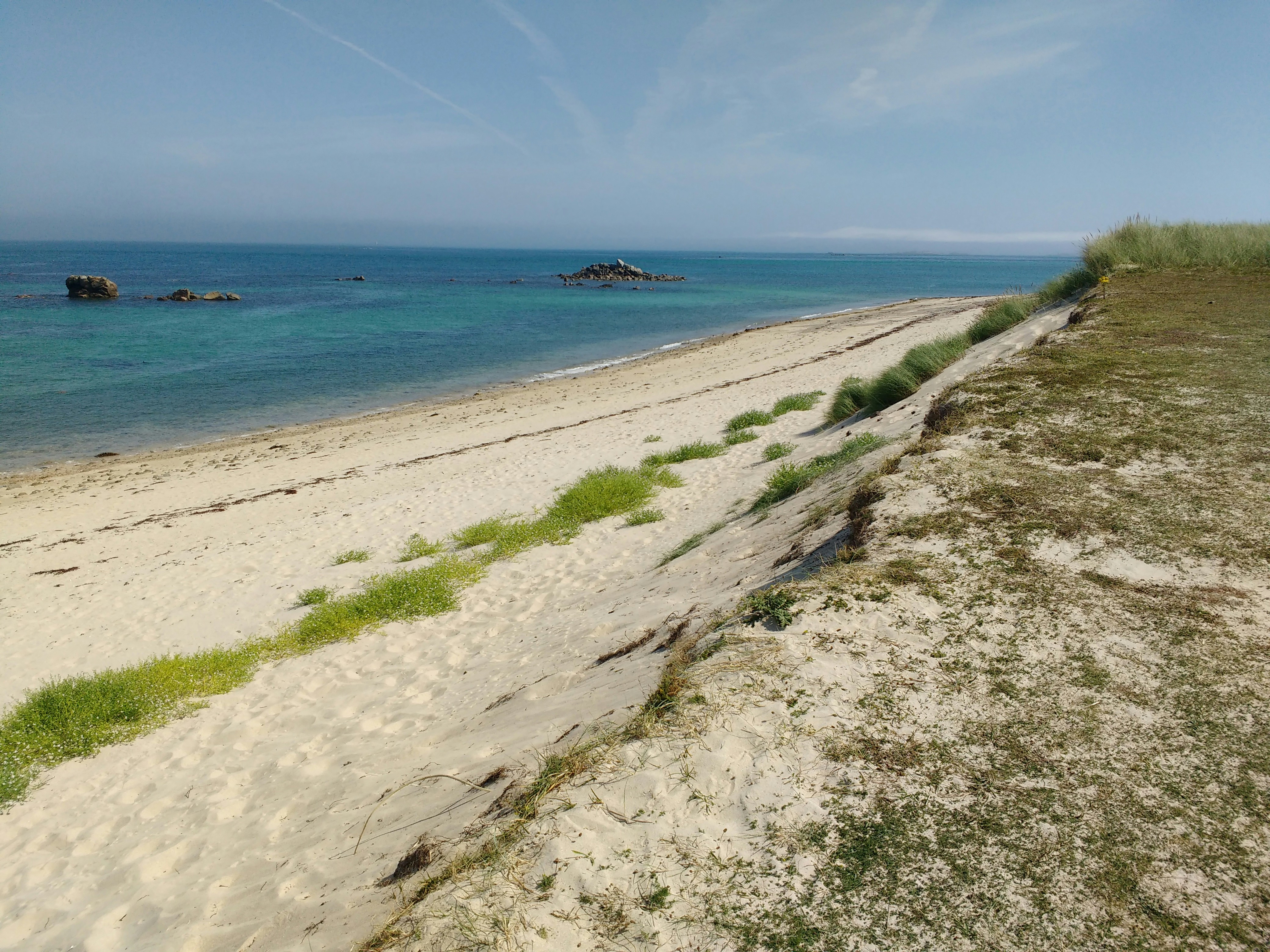Sandy beach with gentle waves and distant rocks under a clear blue sky.