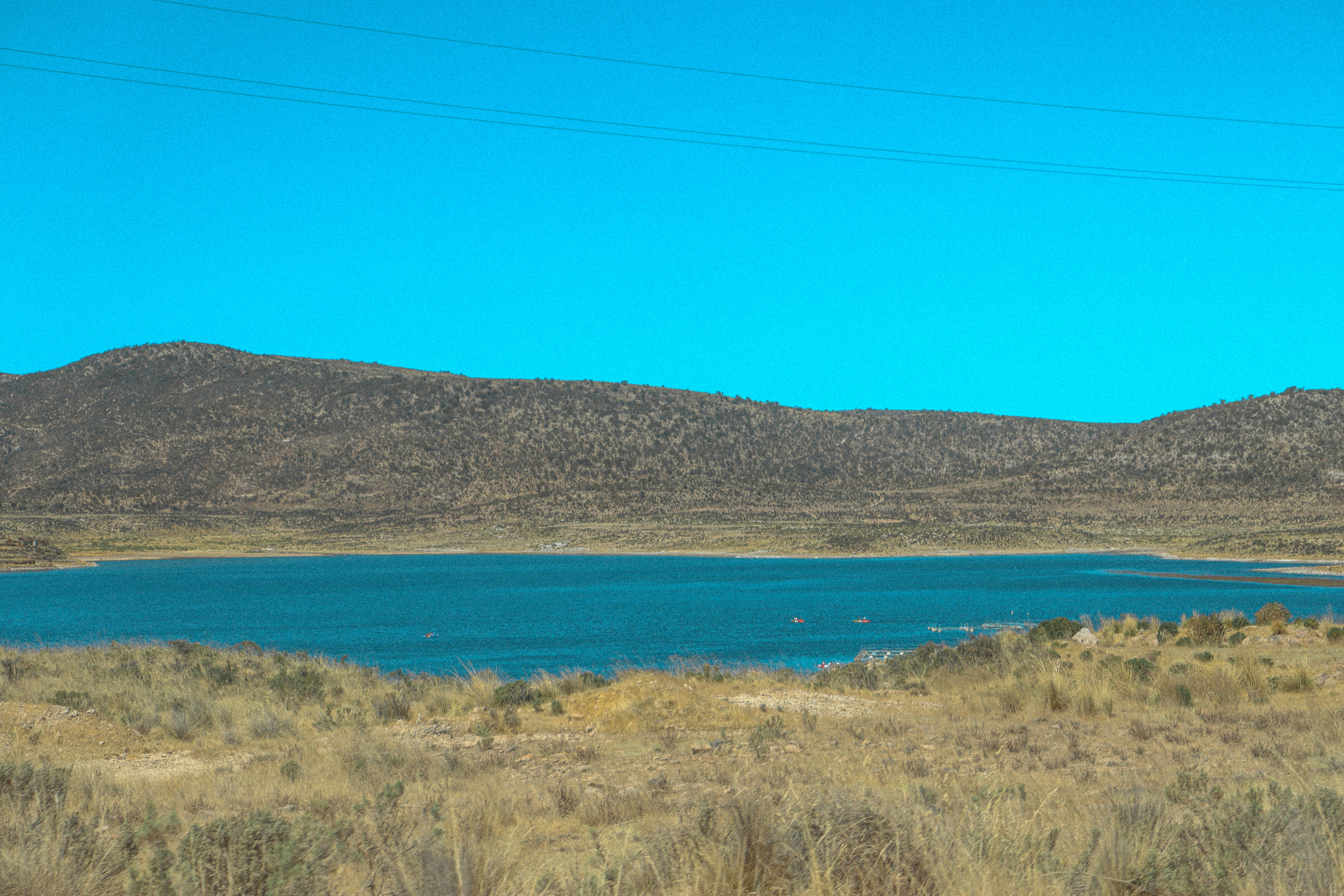 Calm blue lake surrounded by dry, rolling hills under a clear sky.