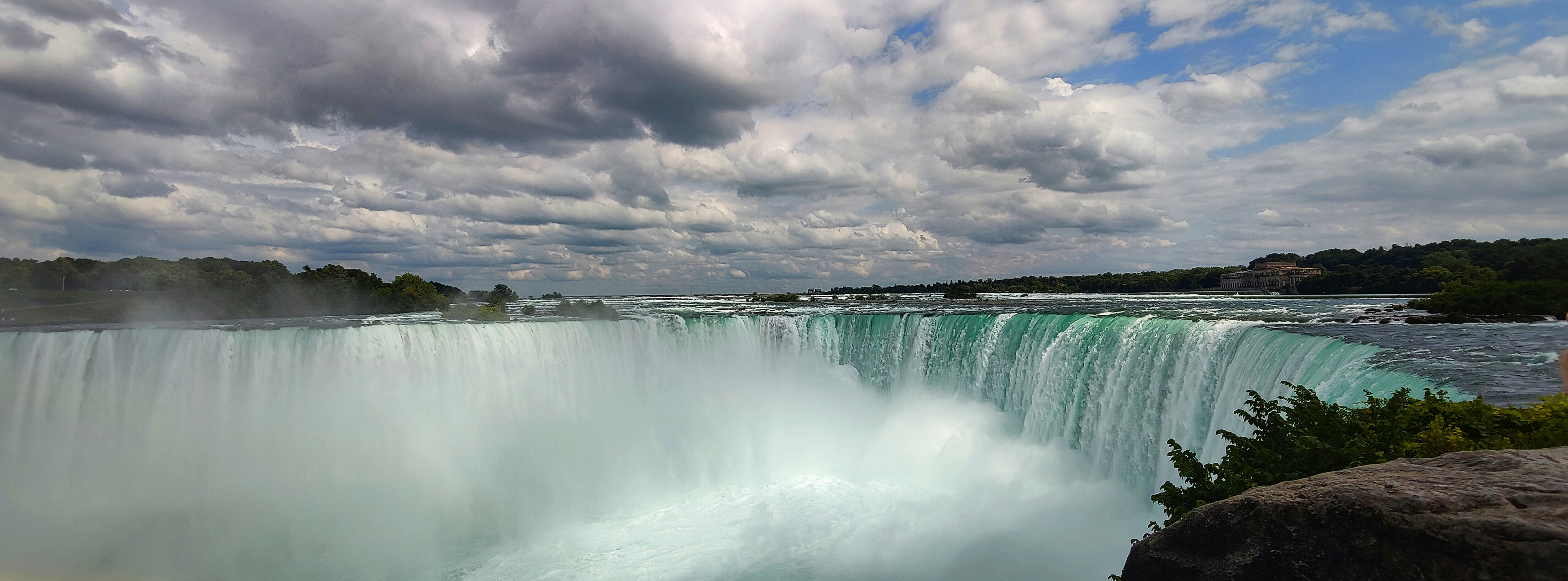 Photograph of a wide waterfall with mist and a cloudy sky.