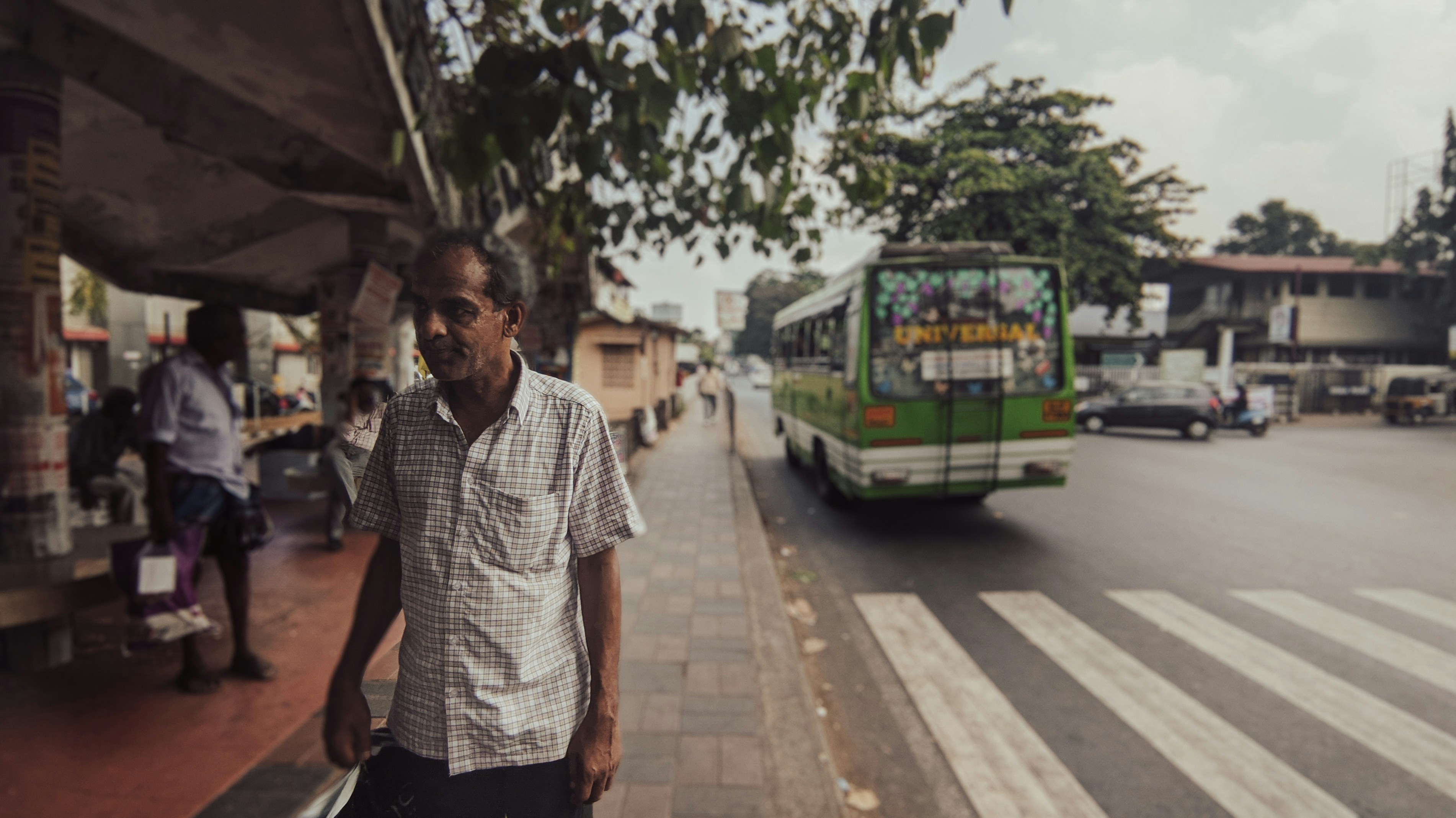 Midday Street Portrait: A Pedestrian Strides Past a Green Bus and Crosswalk