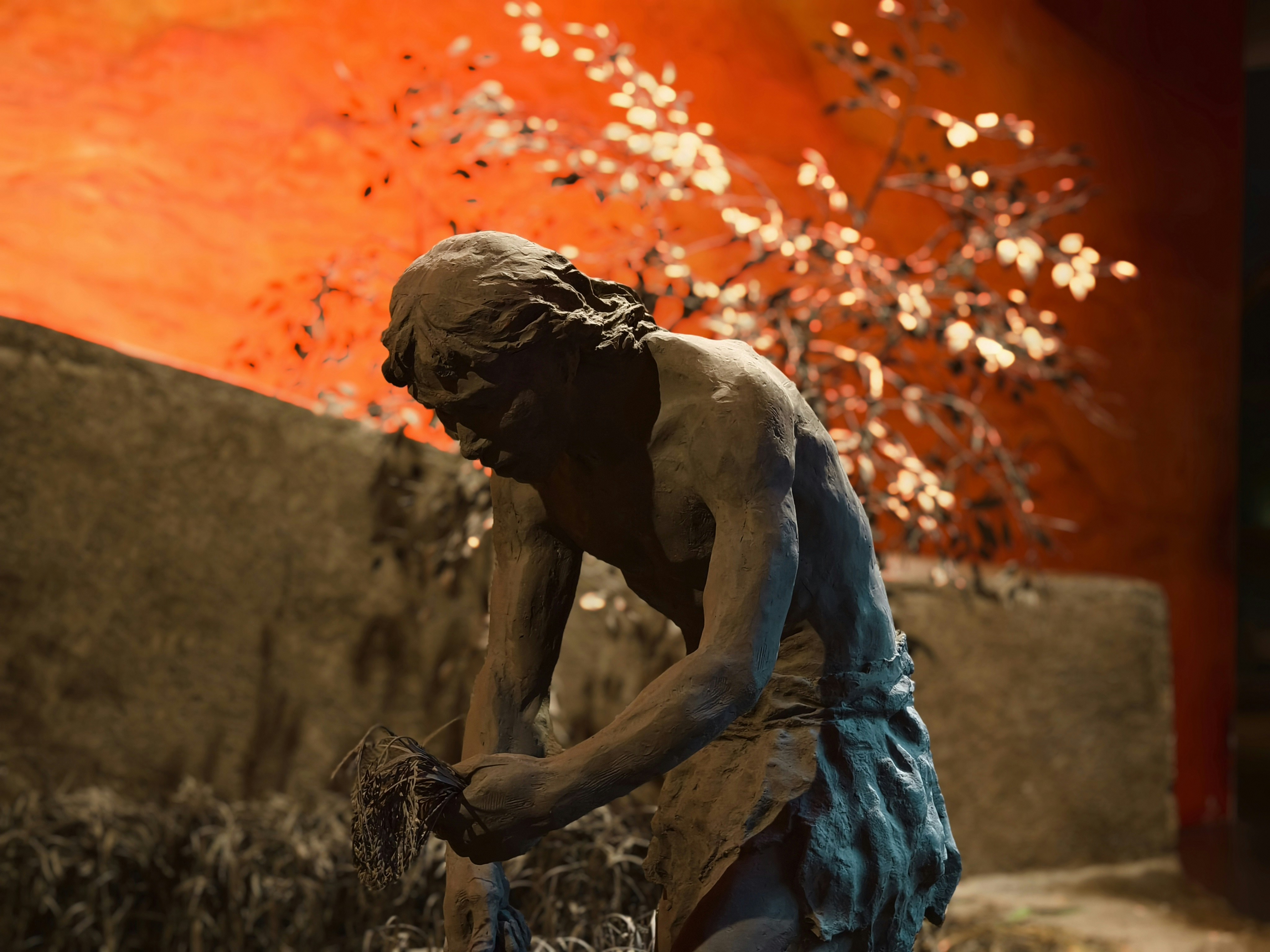 Bronze sculpture of a thoughtful figure with a vibrant red and orange background.