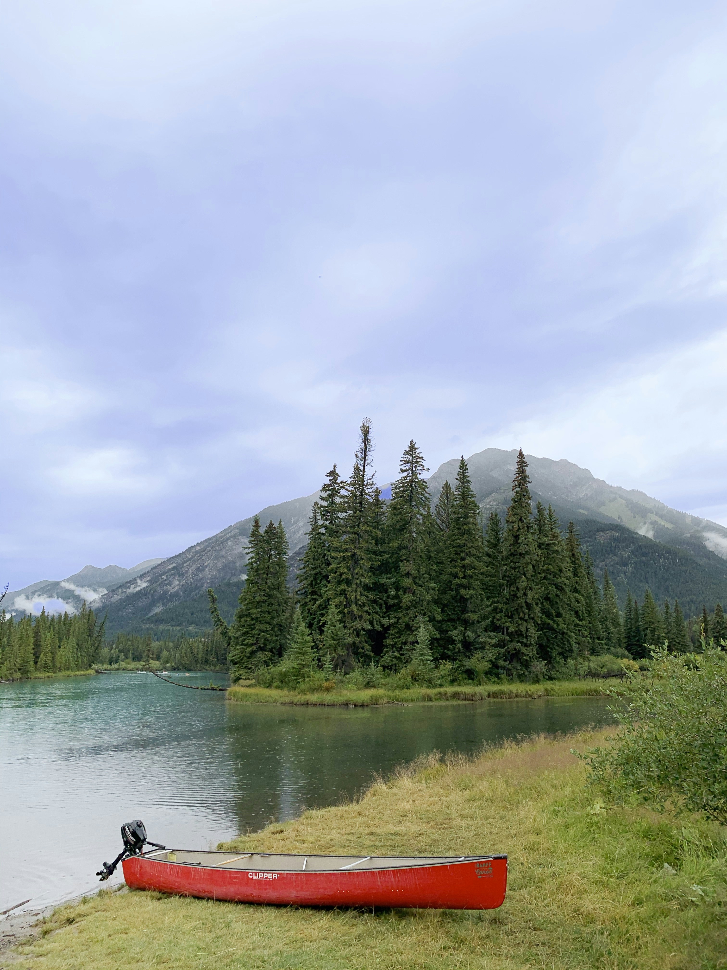 A red canoe sitting on the shore of a lake