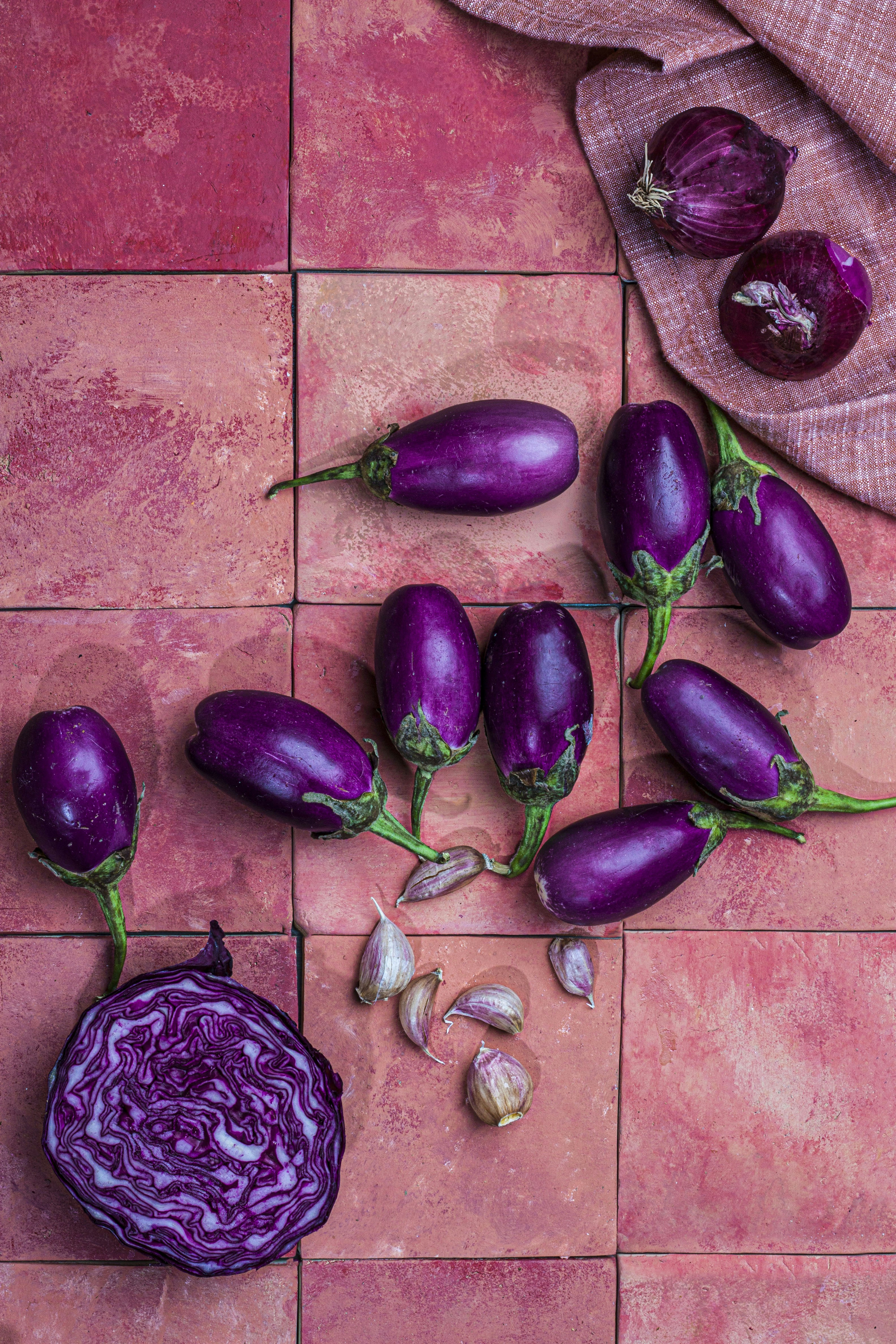 A group of purple eggplant sitting on top of a tiled floor