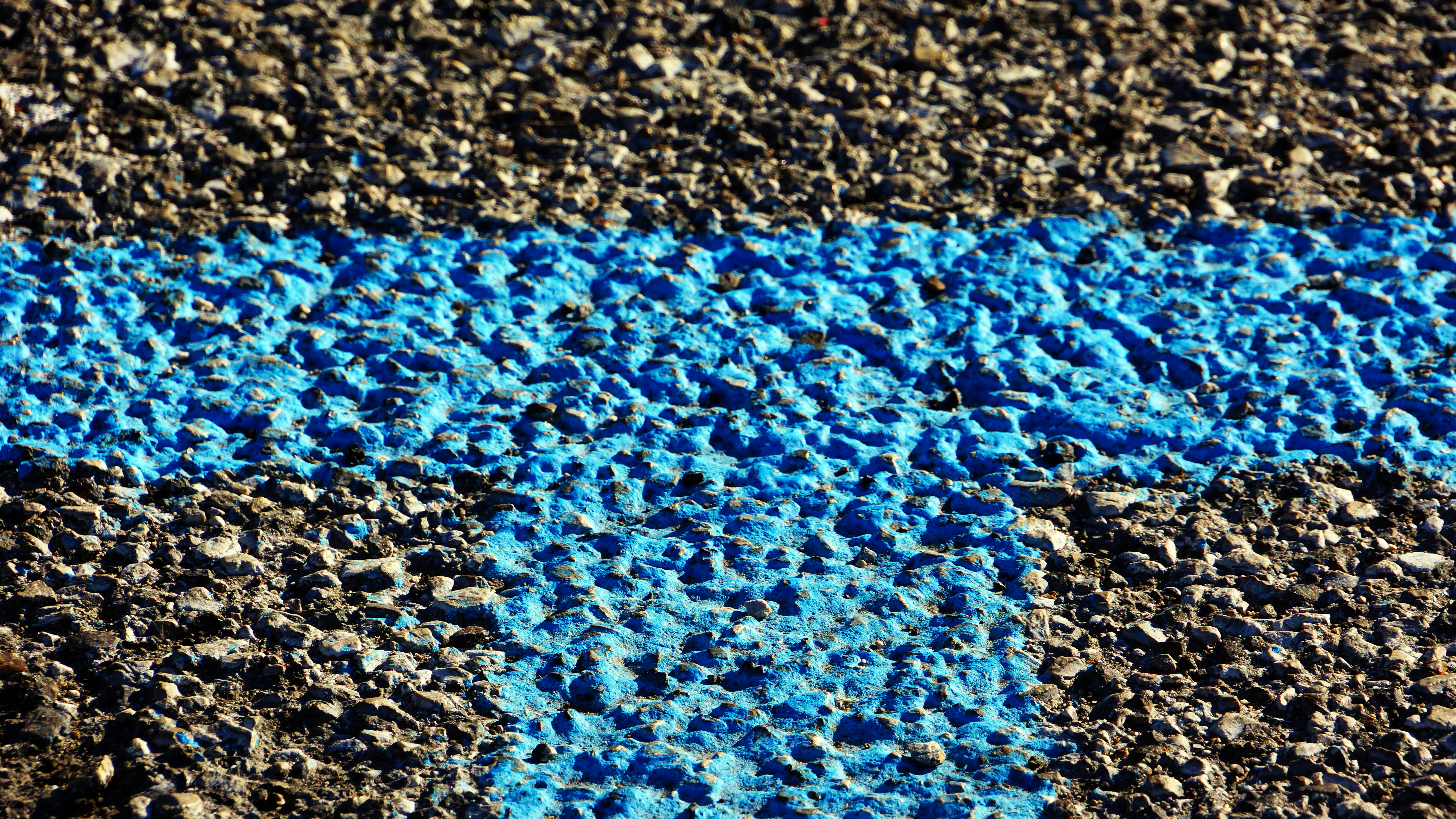 Close-up of a textured asphalt surface with a bright blue painted line crossing it horizontally.