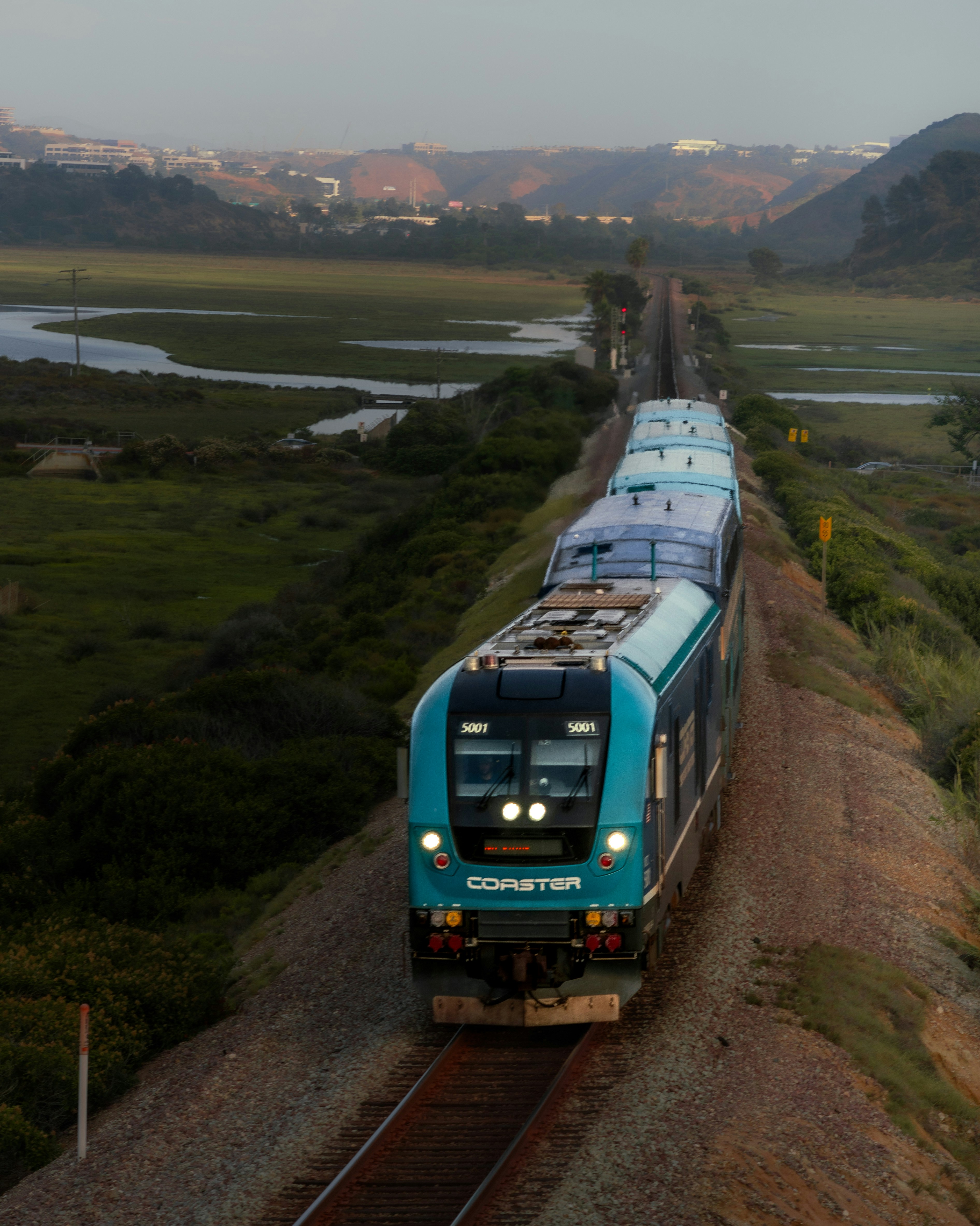 Teal Locomotive: A solitary passenger train threads the marshland spine toward the horizon.