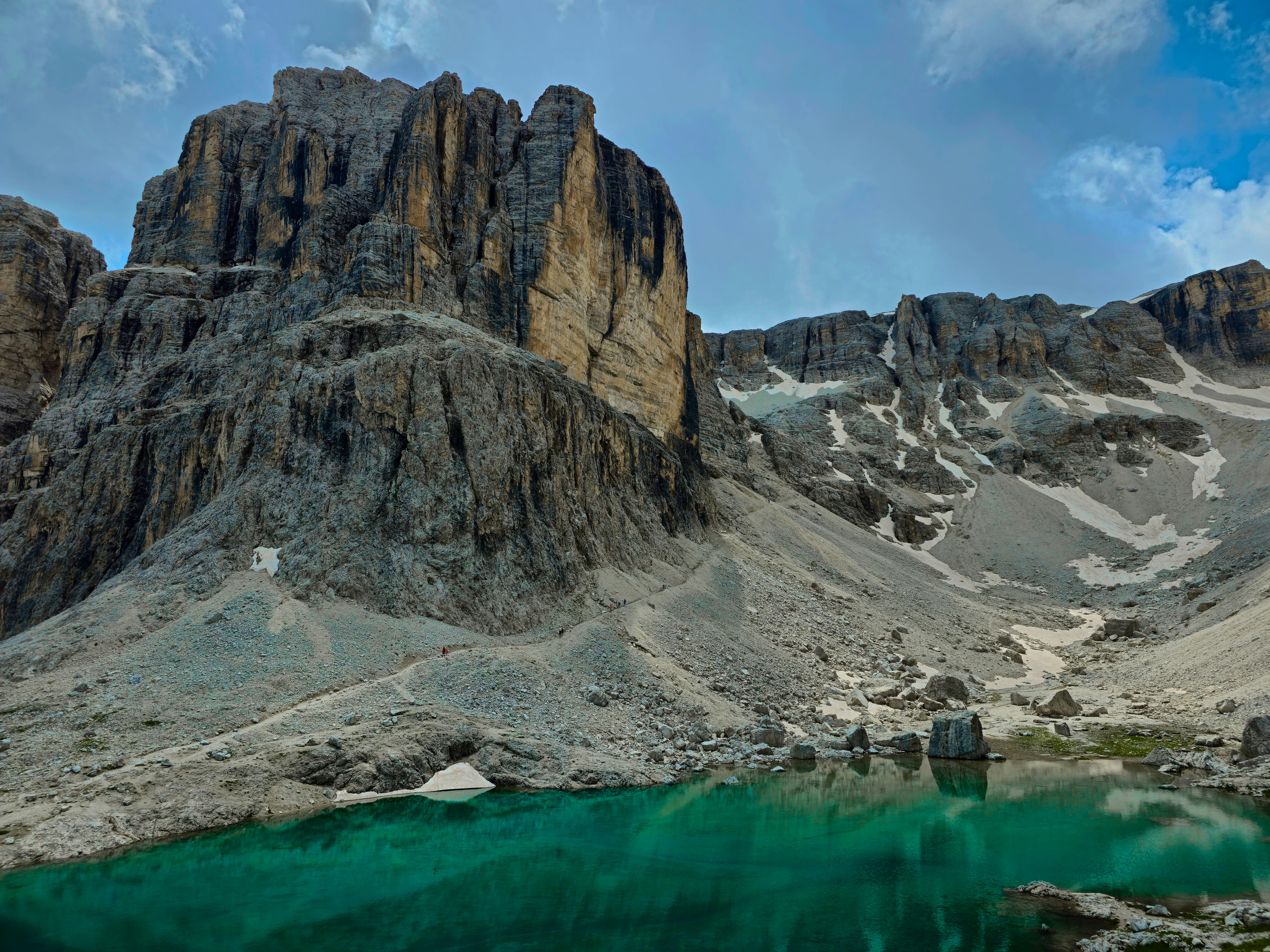 Turquoise alpine lake surrounded by towering rugged cliffs under a partly cloudy sky.