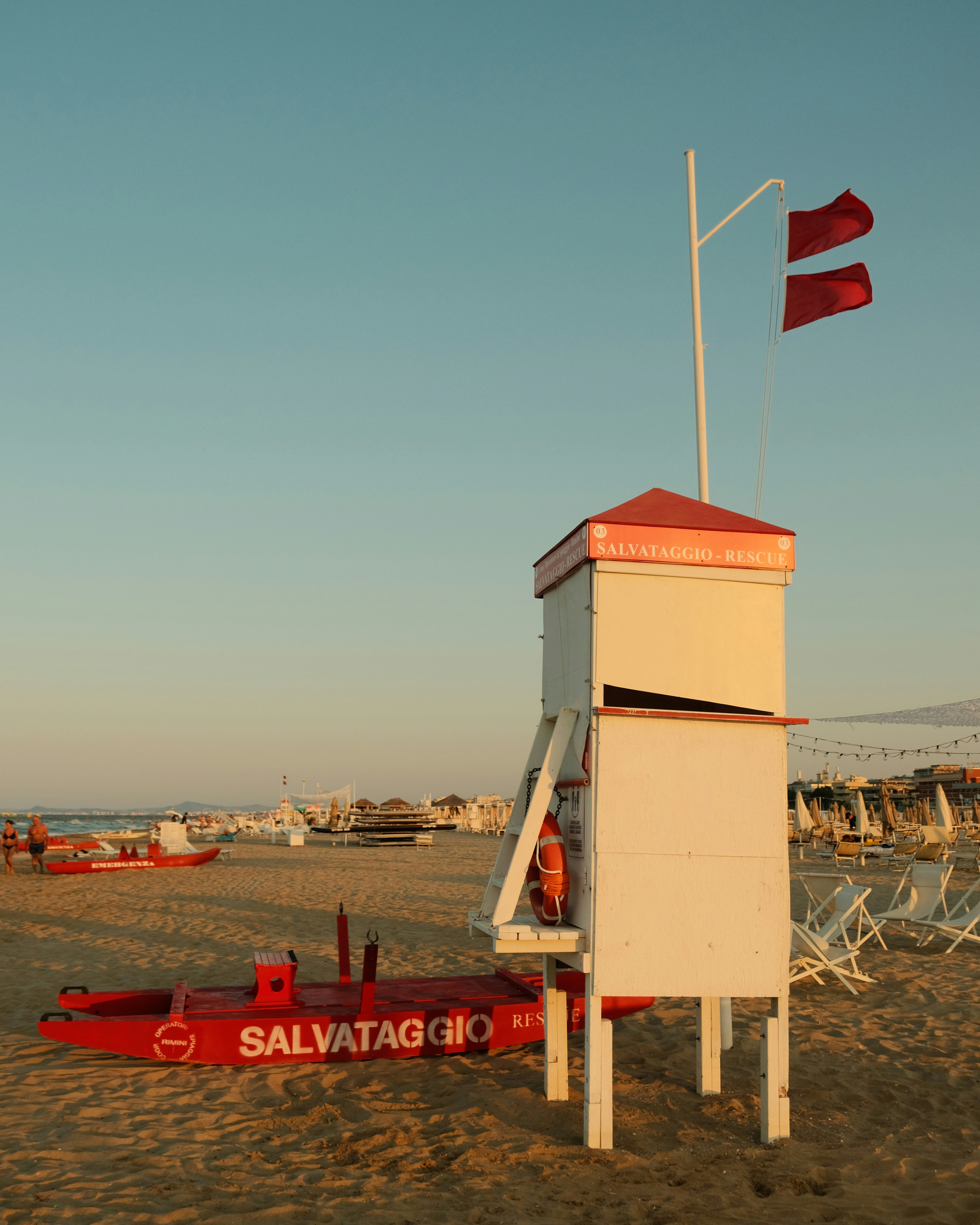 Golden Hour Sentinel: Salvataggio Lifeguard Tower with Red Flags on a Sunlit Beach