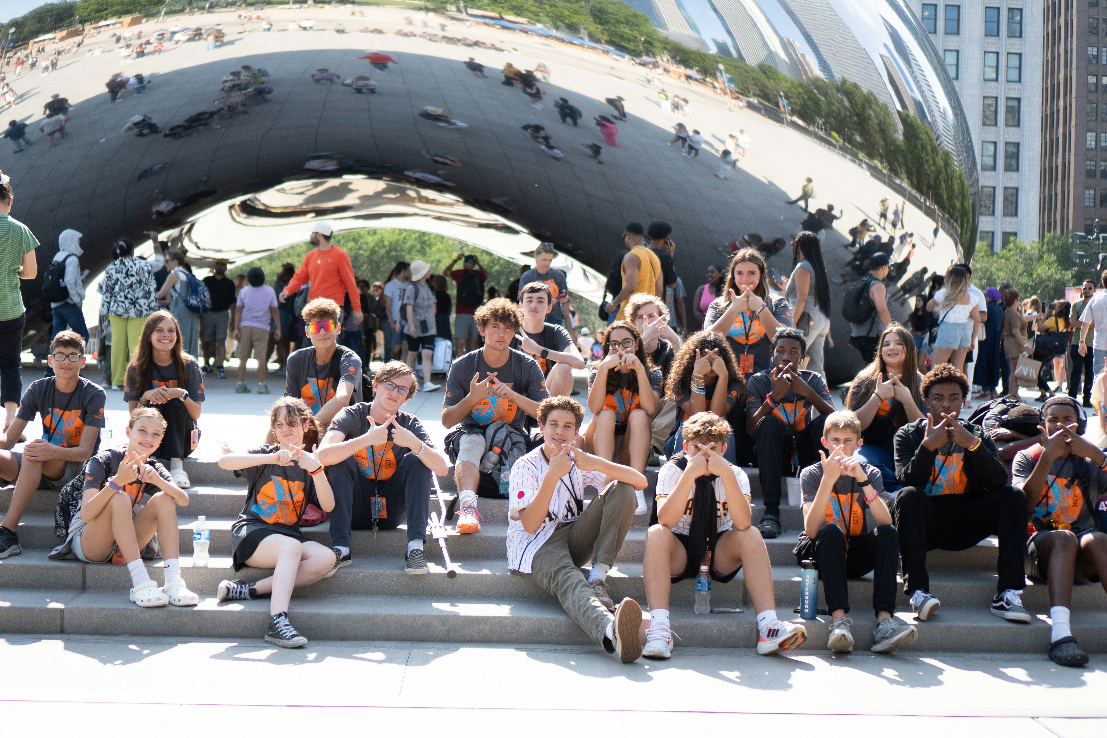 Group of tourists photositting on steps beneath a reflective arch near a glass-building campus