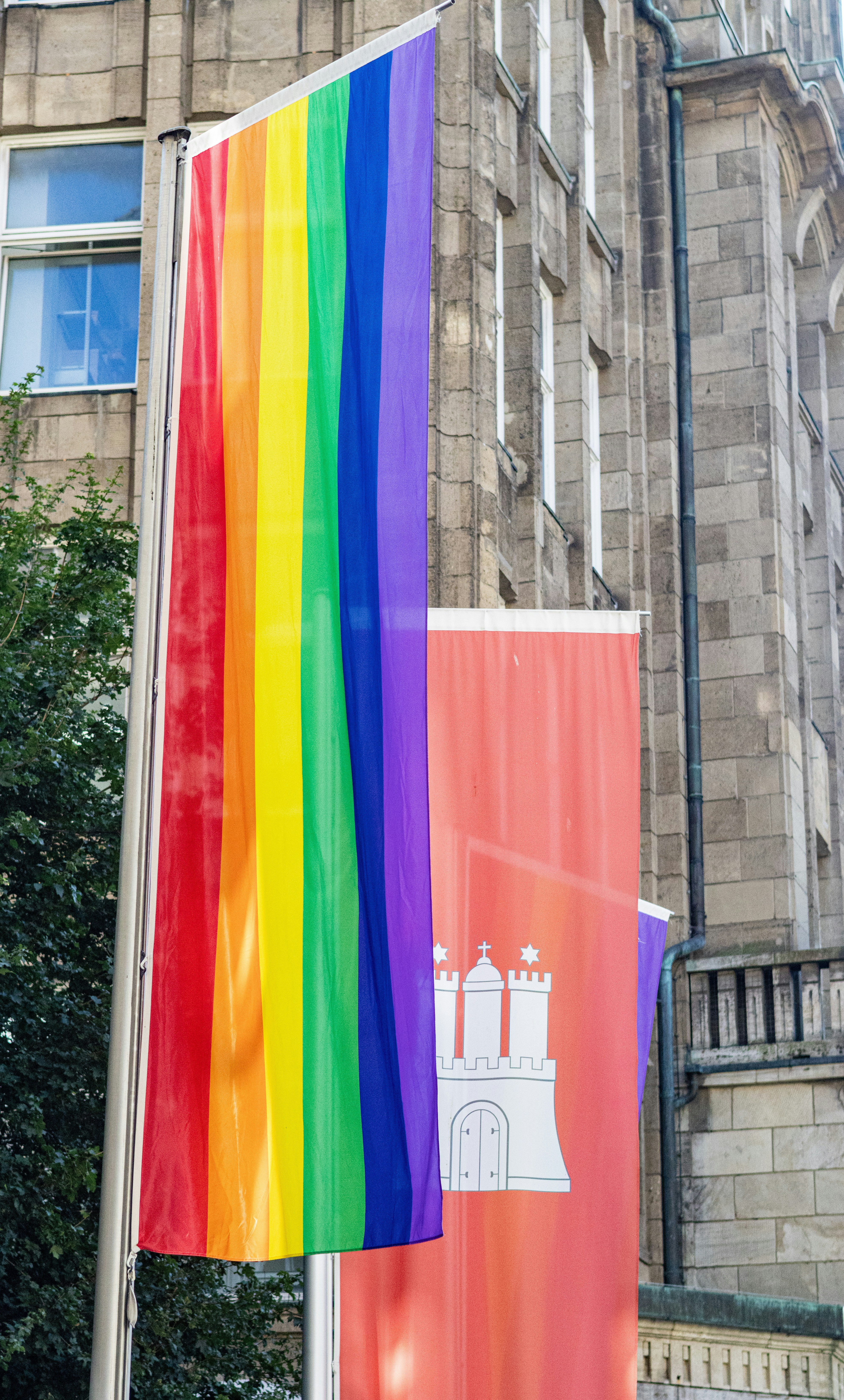 Rainbow on Stone: Pride Flag beside a red banner with a white castle emblem