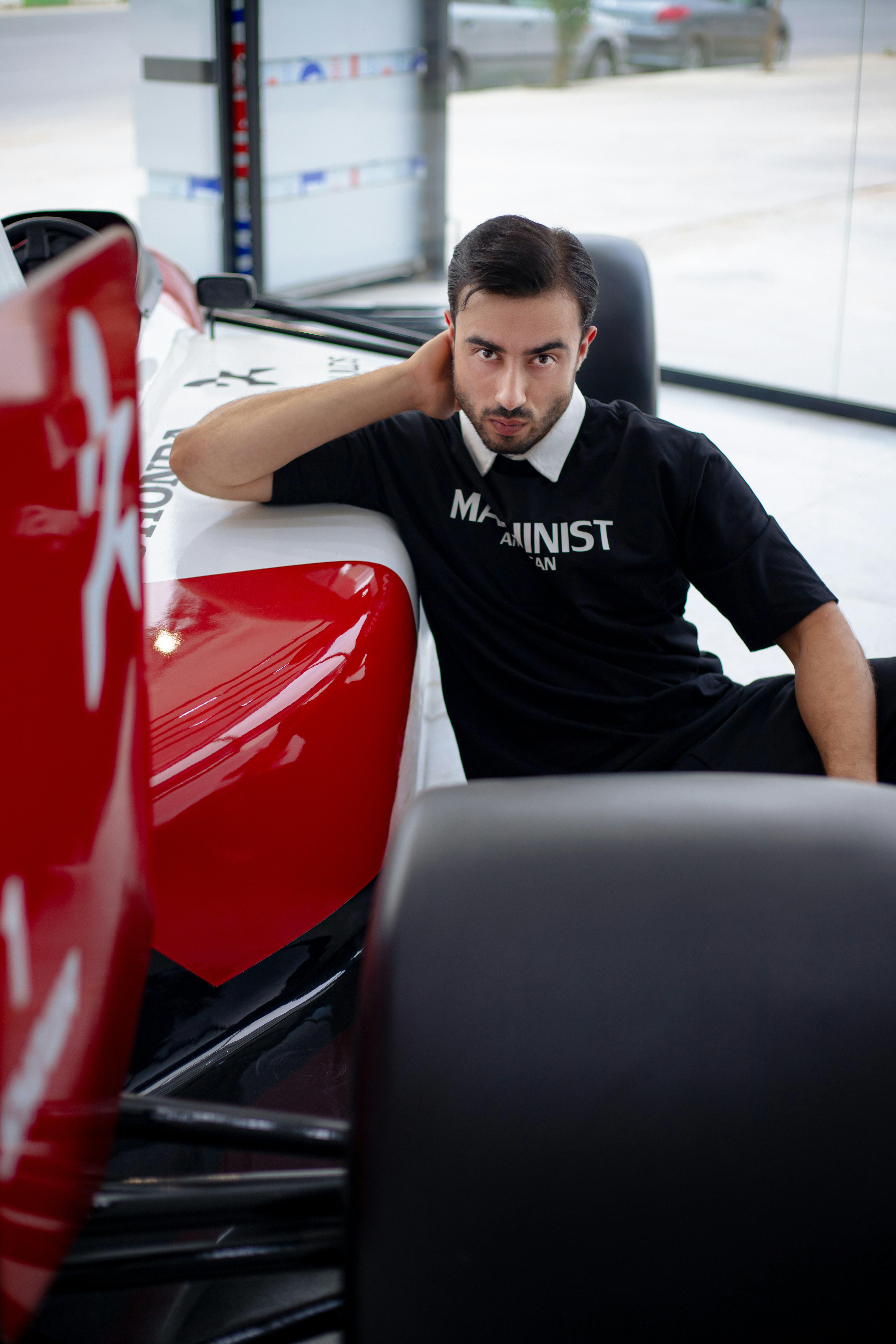 Intense gaze beside a glossy red race car in a sunlit showroom