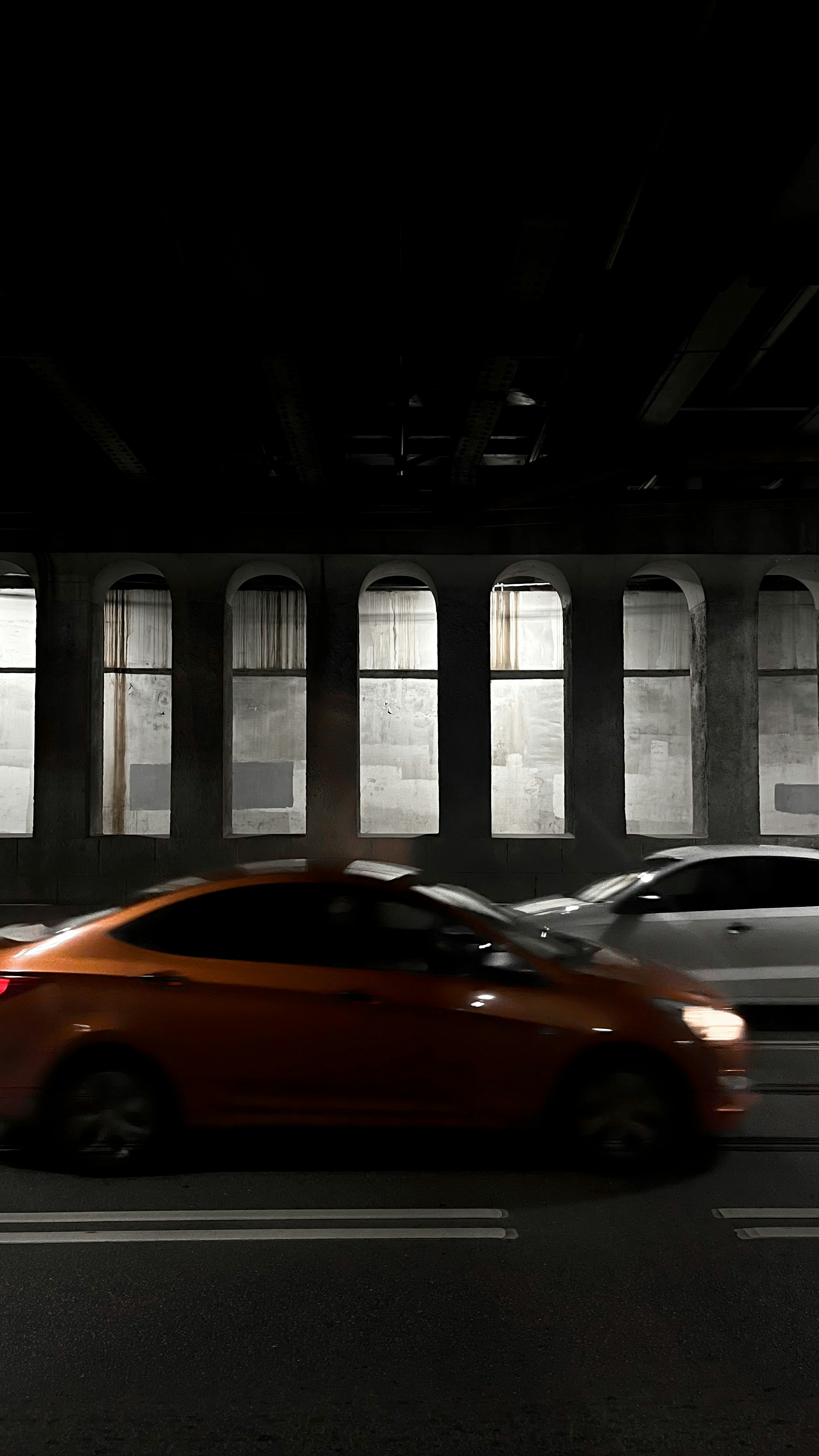 Night Street Ride: Blurred Orange Car Under Dim Arches